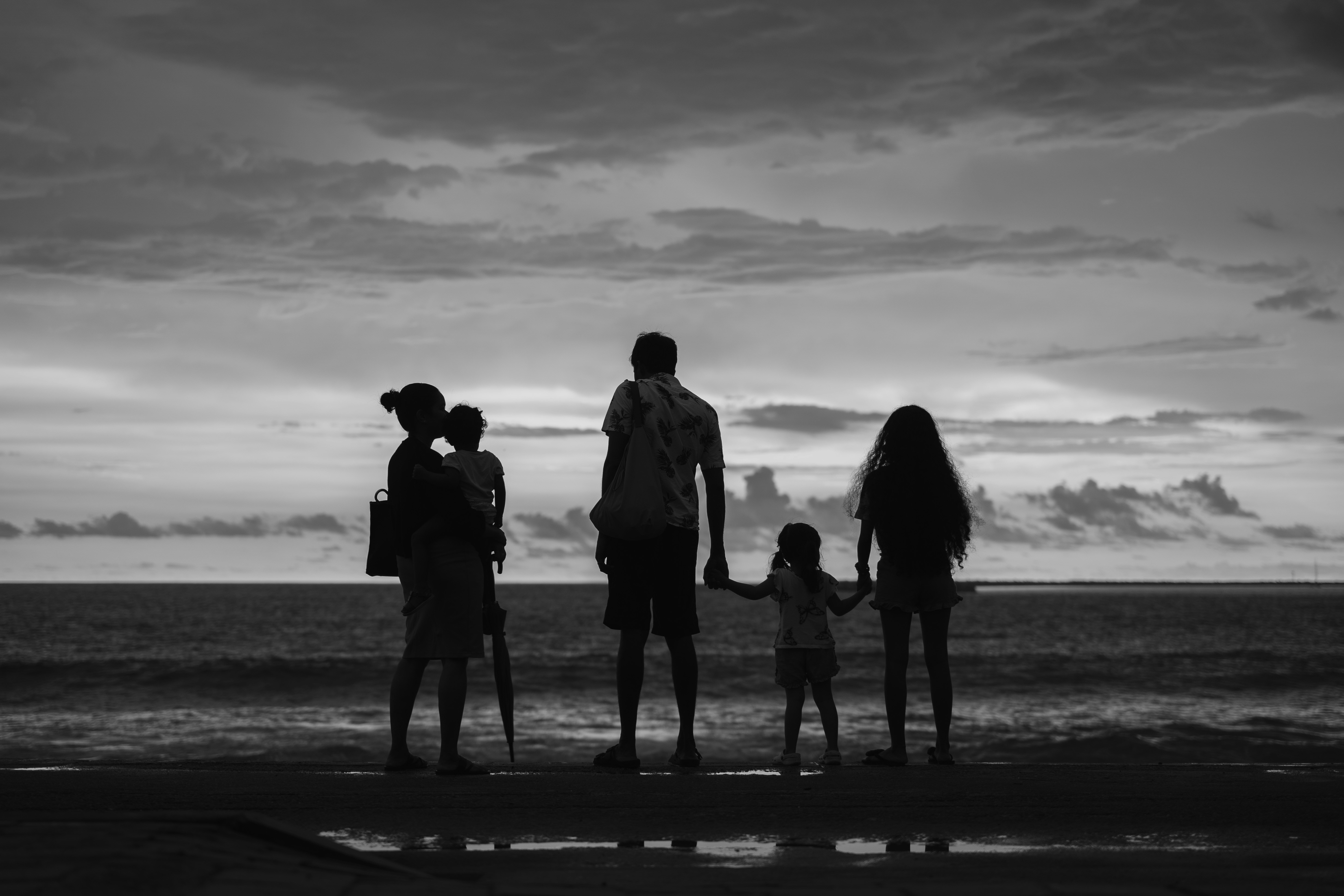 A family of five silhouetted against the ocean at sunset.