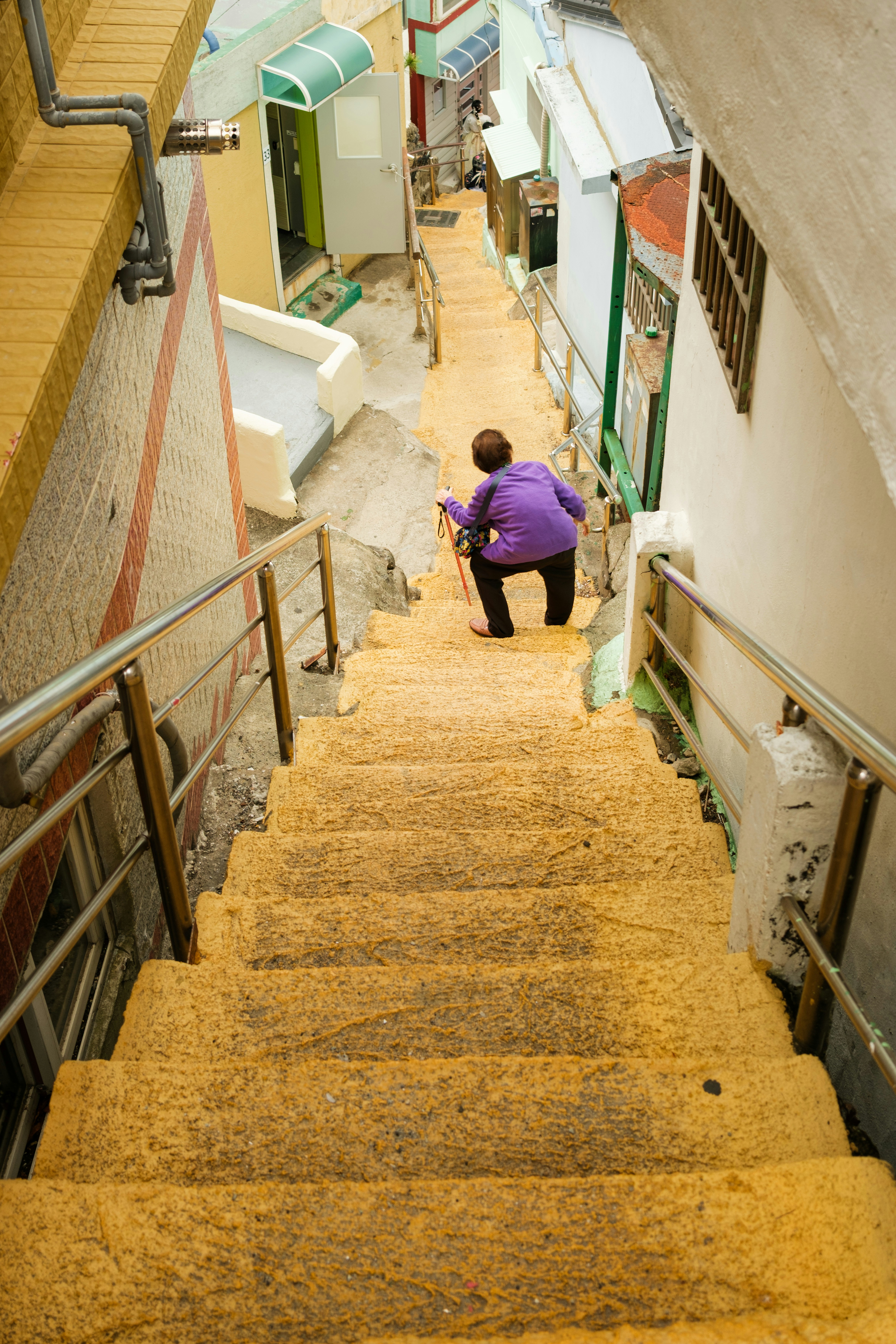 Colorful Descent: A Pedestrian in a Purple Jacket Navigates a Sunlit Stairway