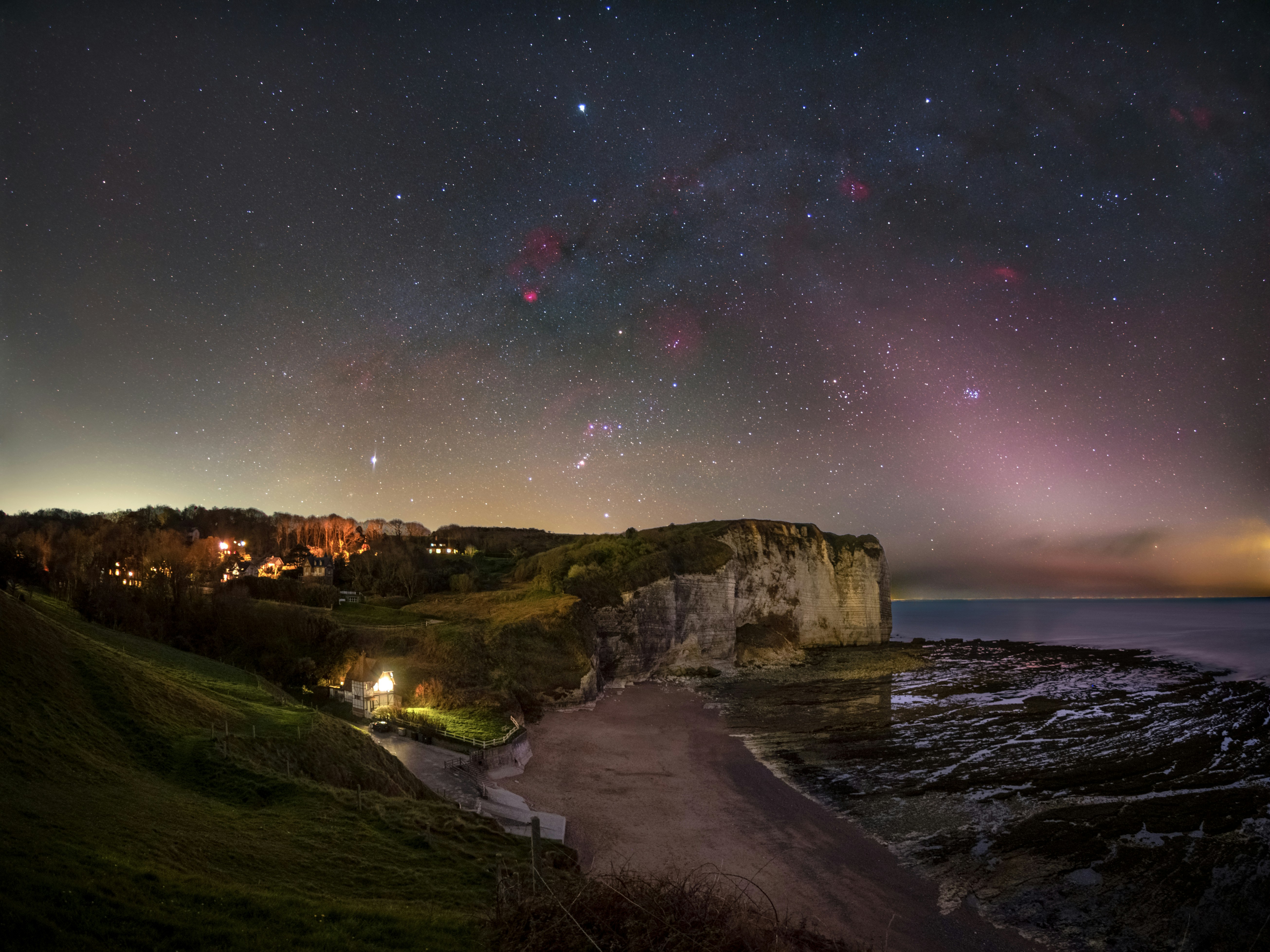 Night sky with stars and aurora over cliffs and beach.