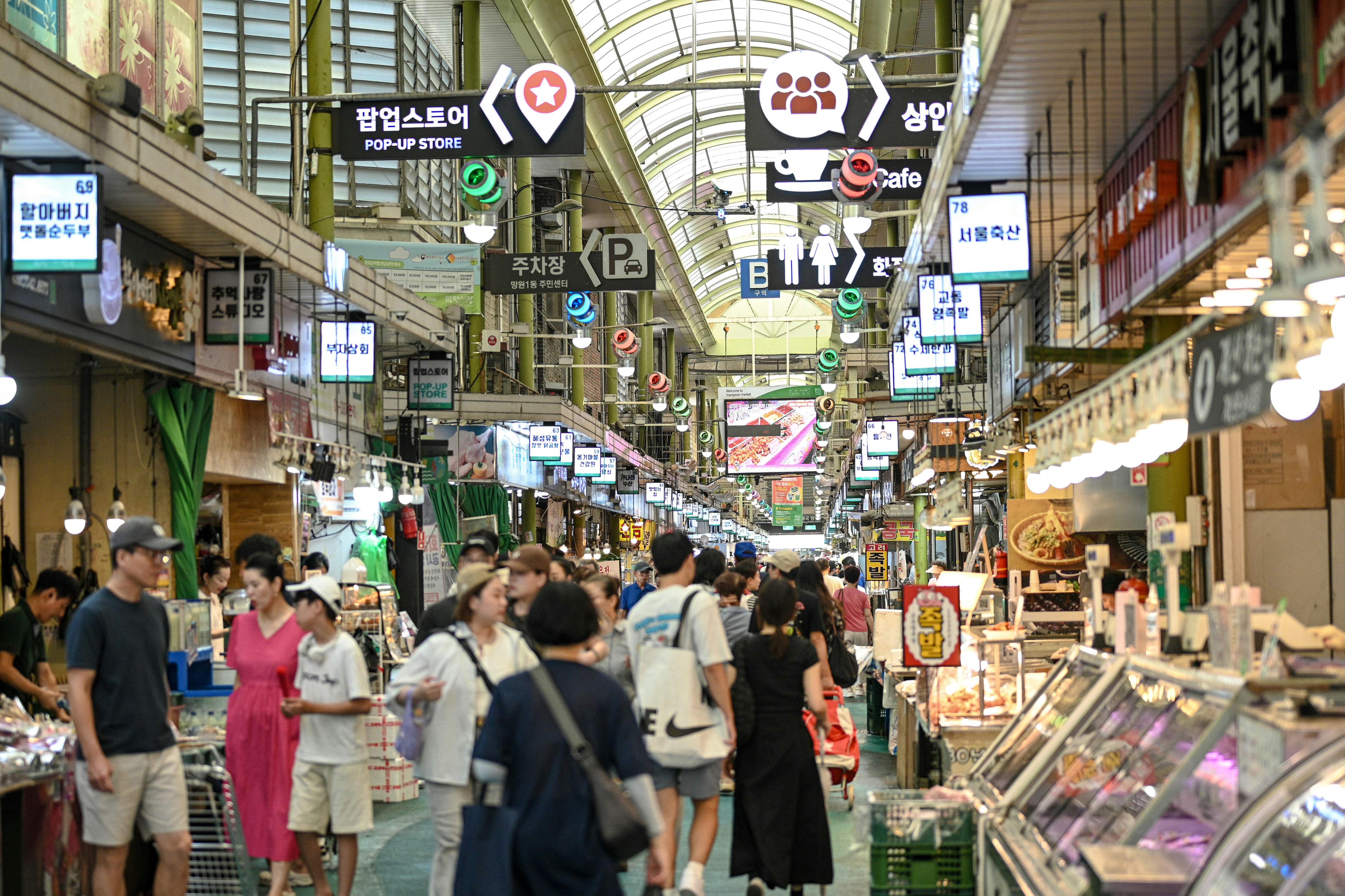 Crowded Market Arcade: Signage, Shoppers, and Stalls Under Arched Skylight
