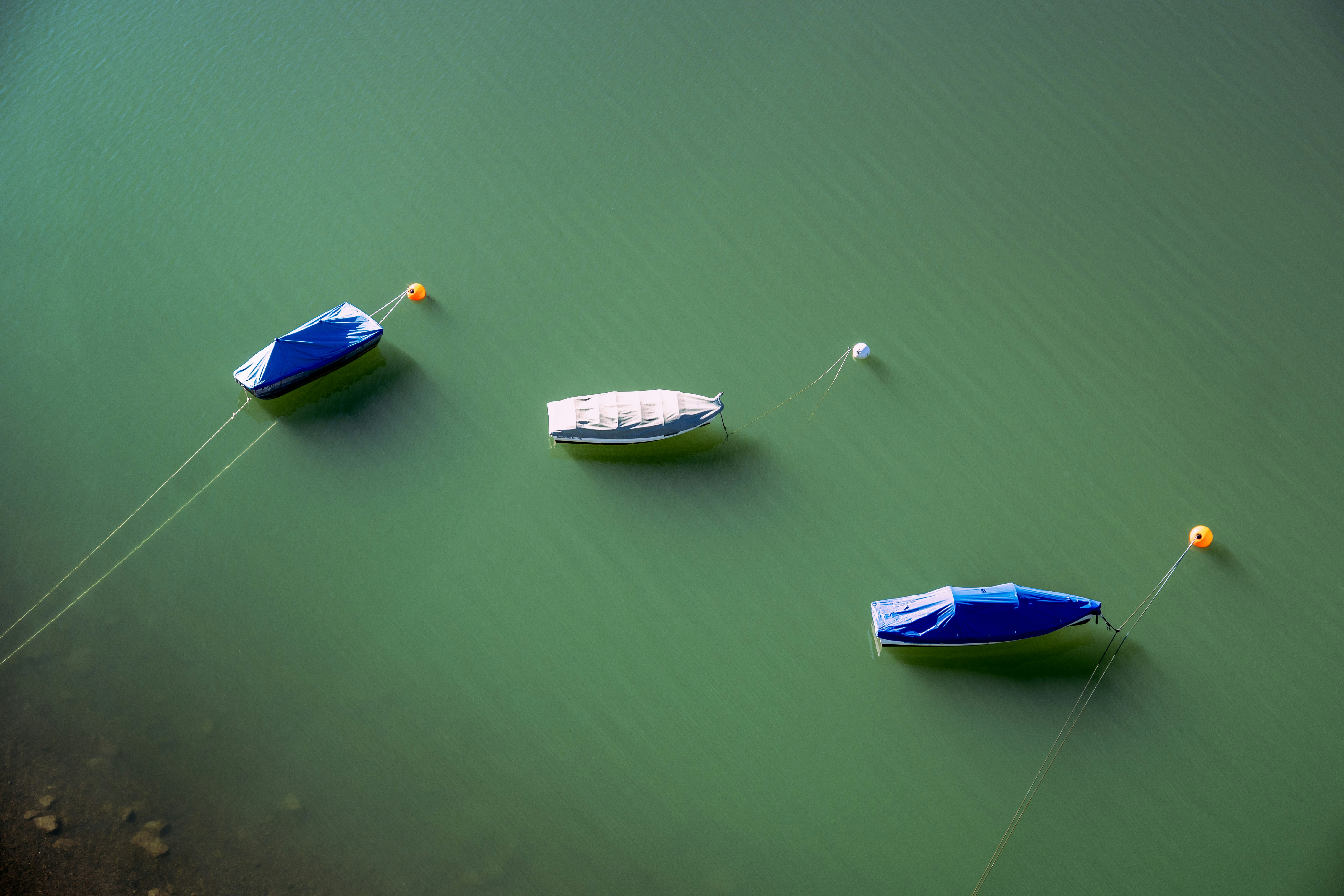 Three small boats drift on green water with mooring lines extending outward, creating a minimalist seascape composition.