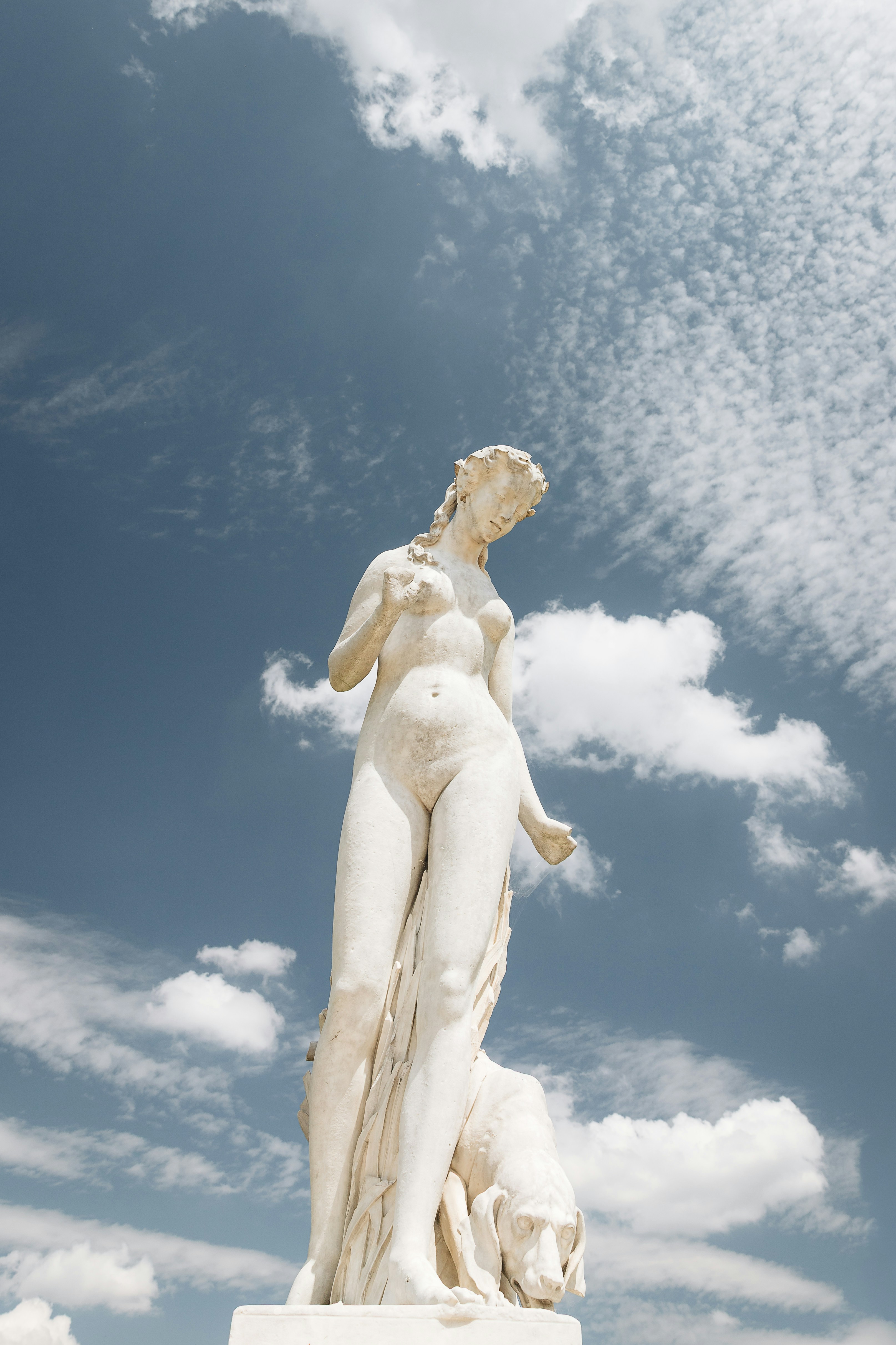 Nude marble statue beneath a sky of drifting clouds