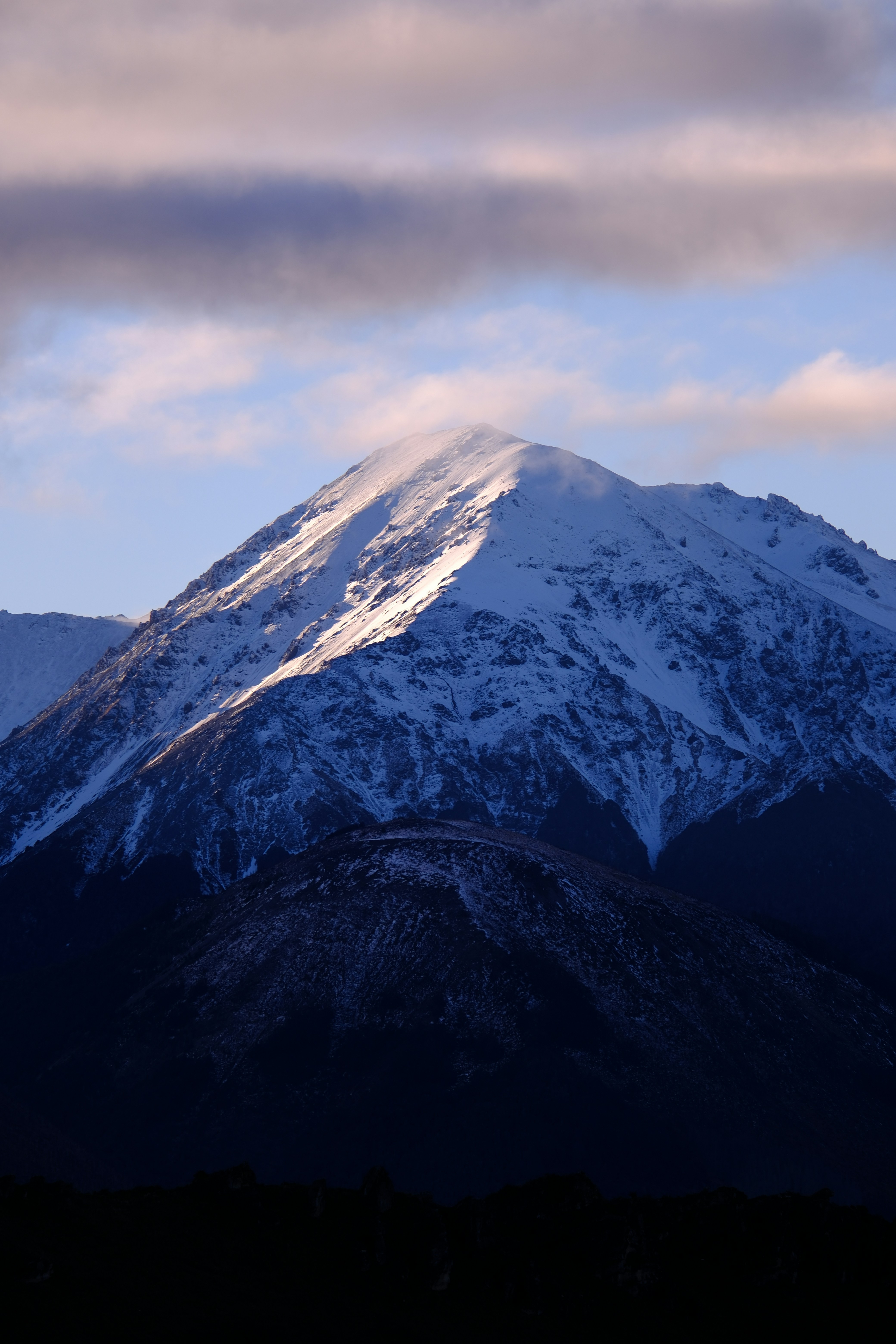 Peak in Pastel Light: A Snow-Capped Summit Under Soaring Clouds