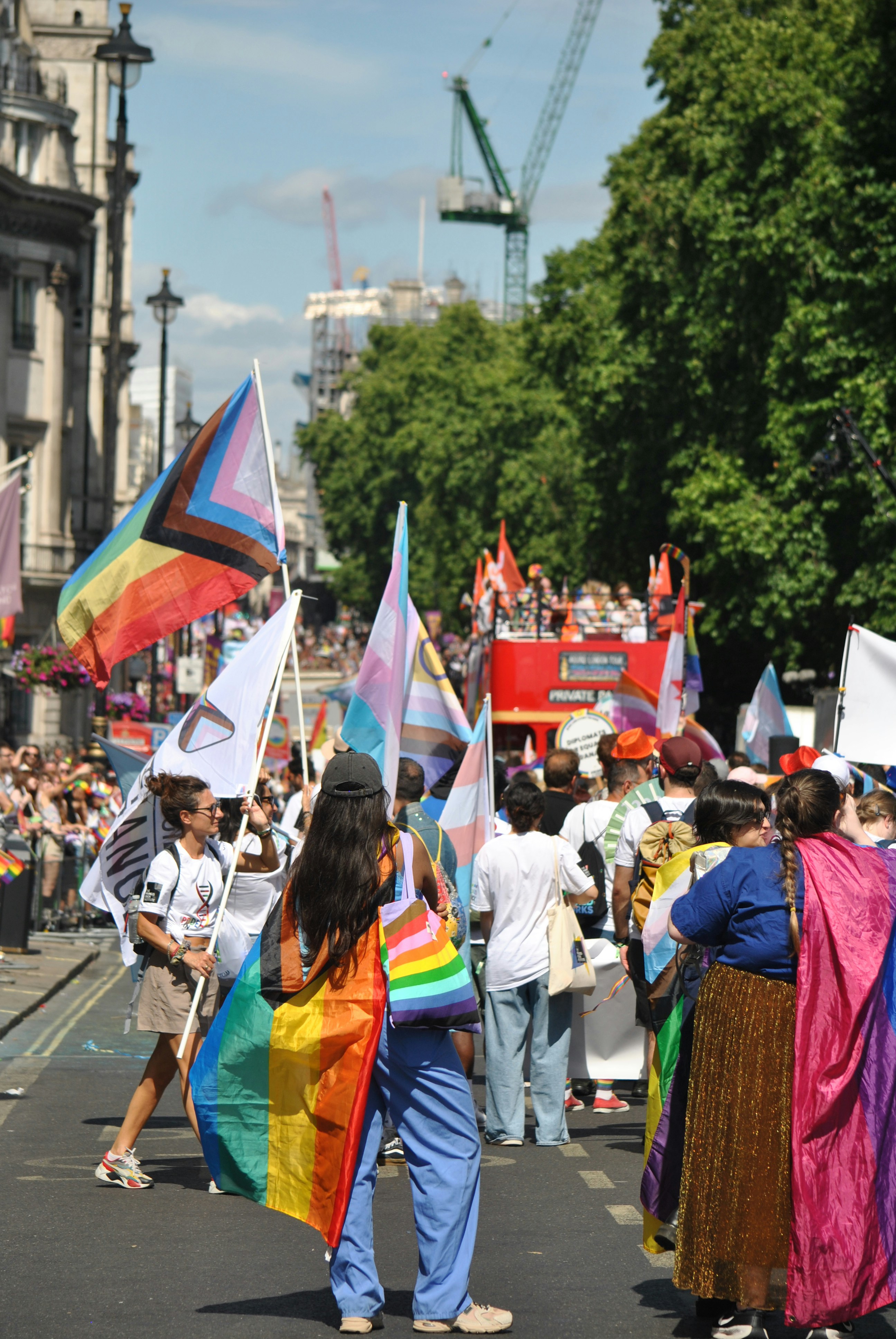 Vibrant parade scene with diverse participants carrying rainbow flags along a city street, flags and colorful garments filling the frame.