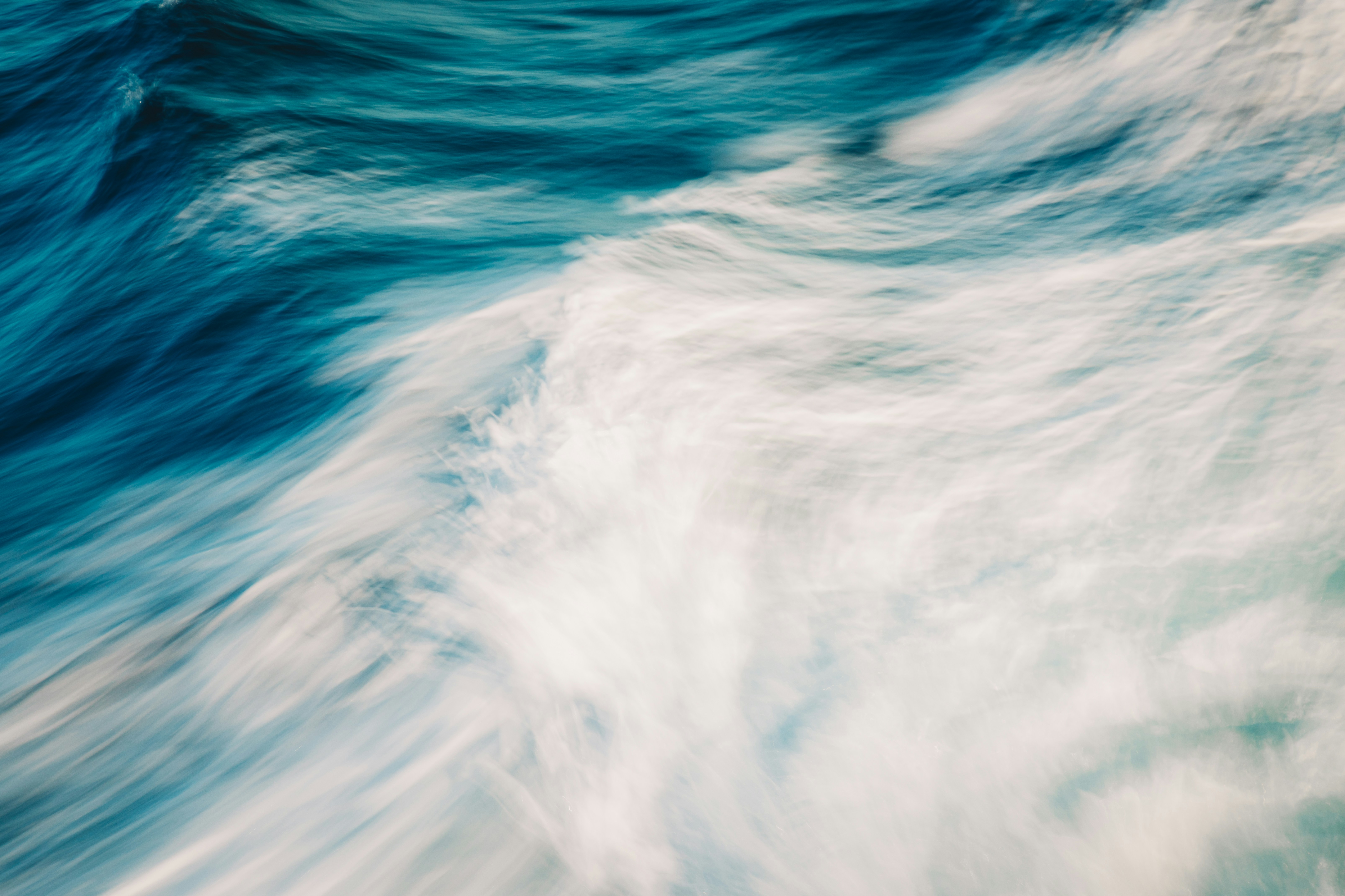 Abstract long-exposure view of deep blue ocean waves trailing behind a boat, capturing the movement and energy of the Mediterranean Sea