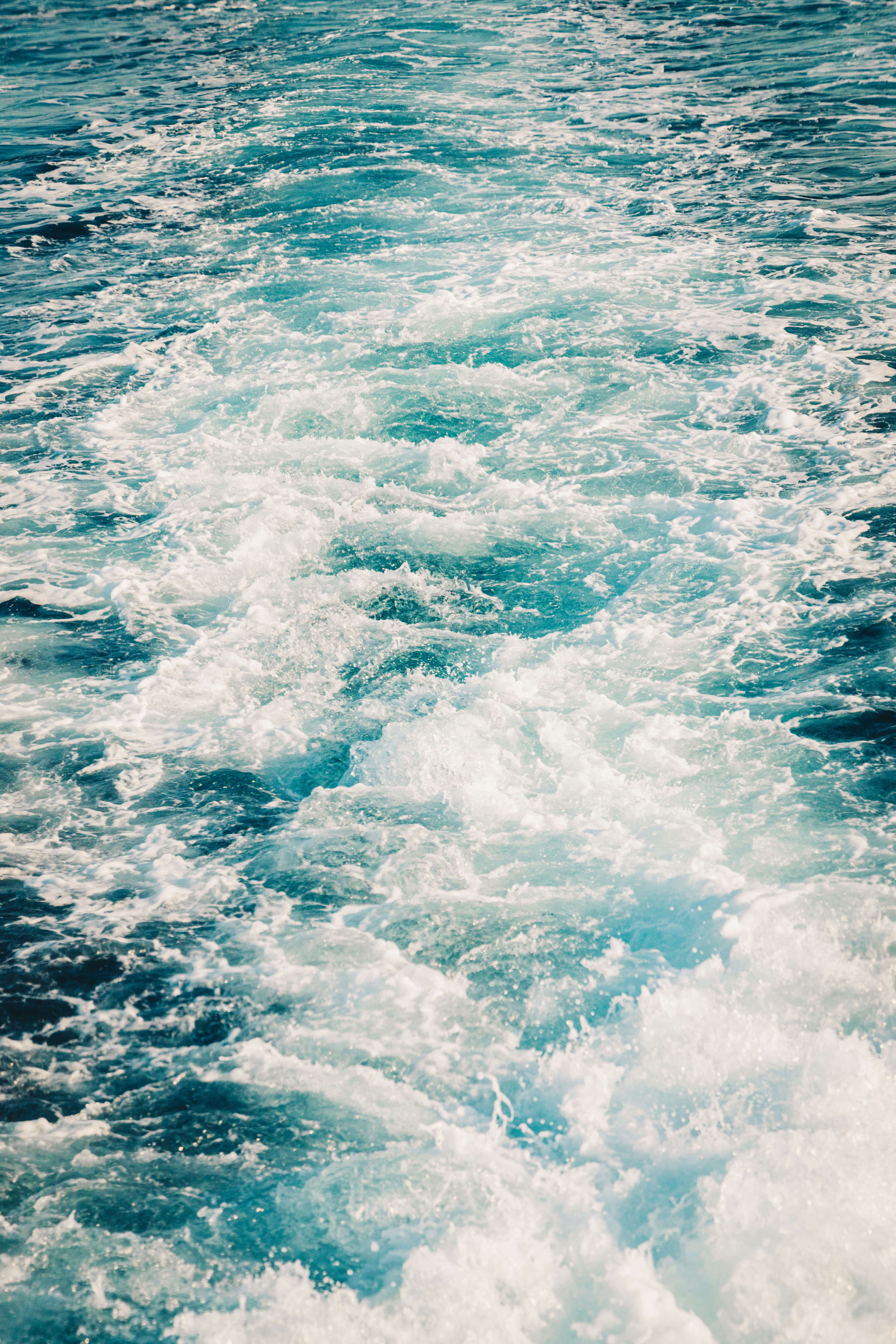 Foaming turquoise boat wake cutting through the Mediterranean Sea, creating a dynamic natural water texture under bright summer light