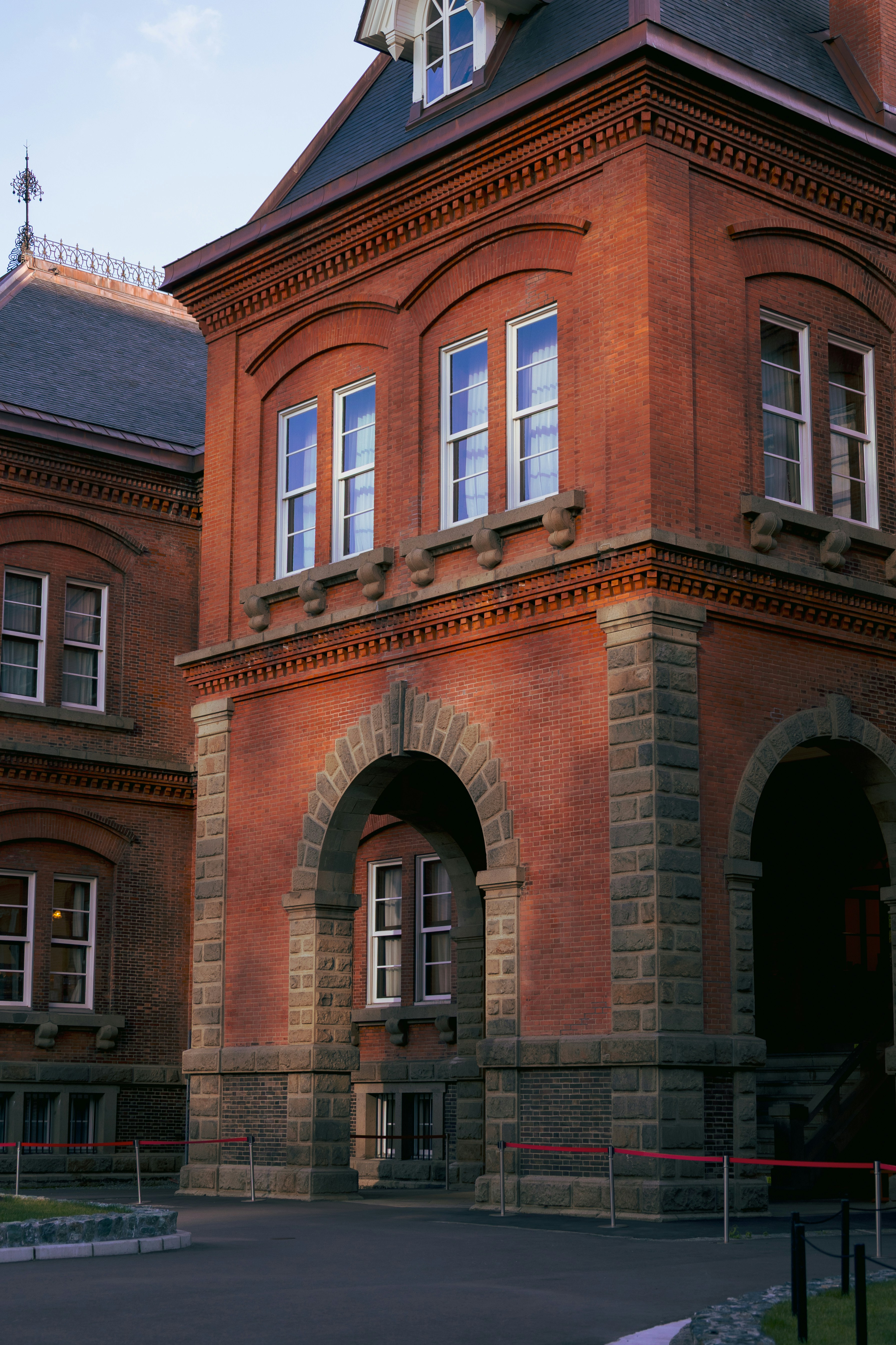 Brick arches and stone detailing of a historic building glow in warm light, highlighting the textured facade and windows; architectural exterior shot with clear foreground paving.