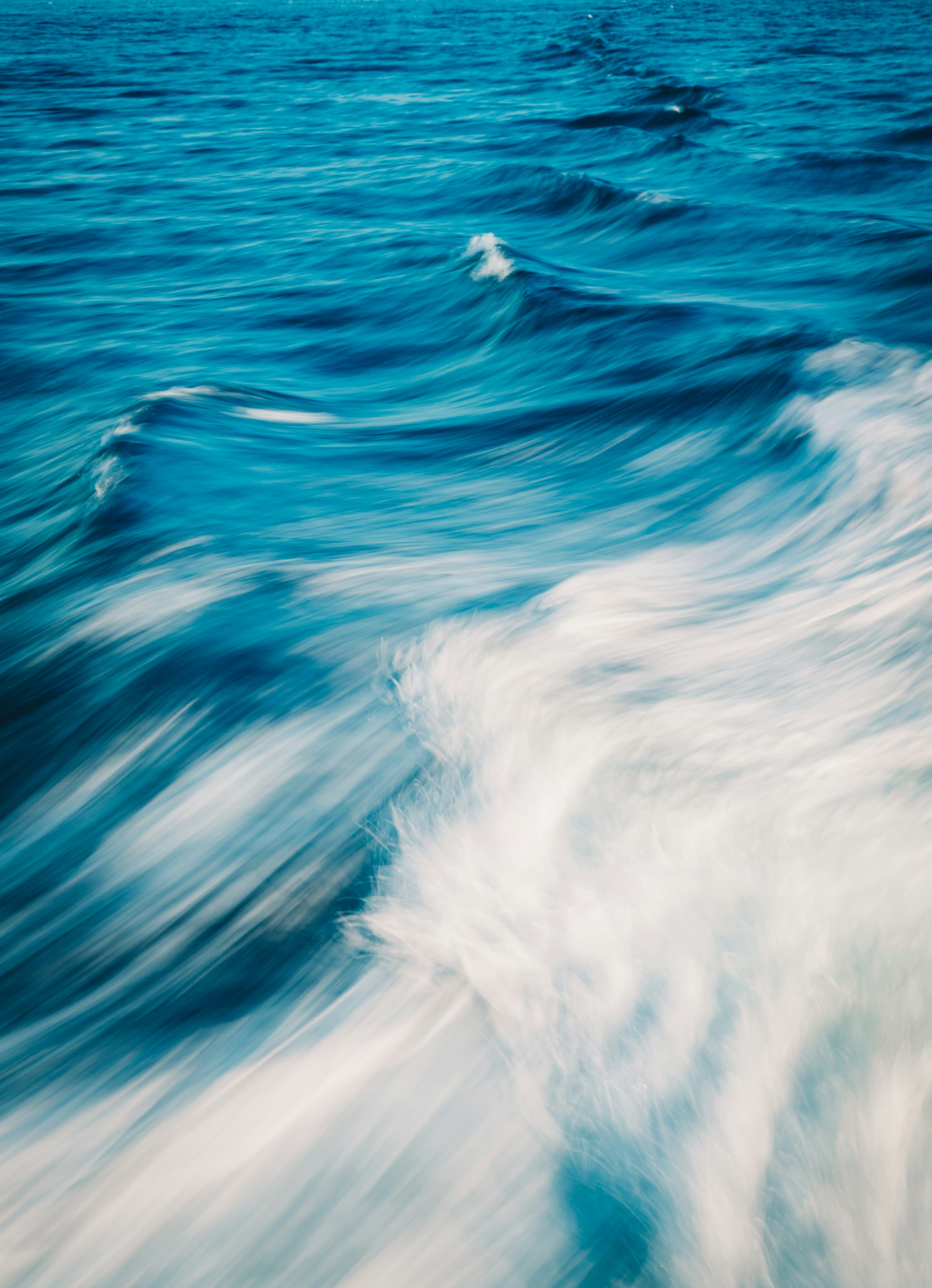 Abstract long-exposure view of deep blue ocean waves trailing behind a boat, capturing the movement and energy of the Mediterranean Sea