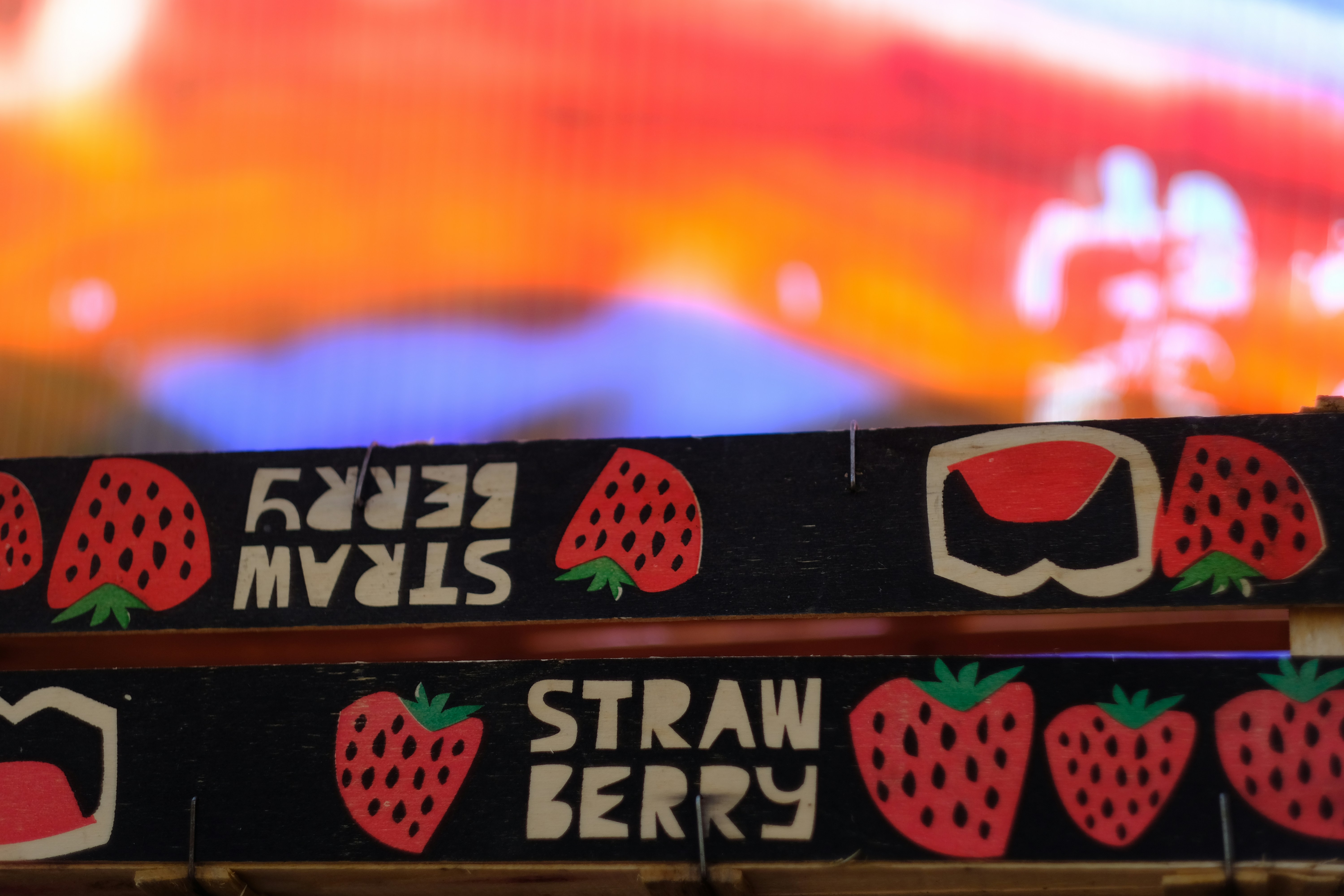 Bright strawberry-pattern packaging stacked along a black surface with bold white text; appears to be fruit snack packaging and a glossy, colorful backdrop.
