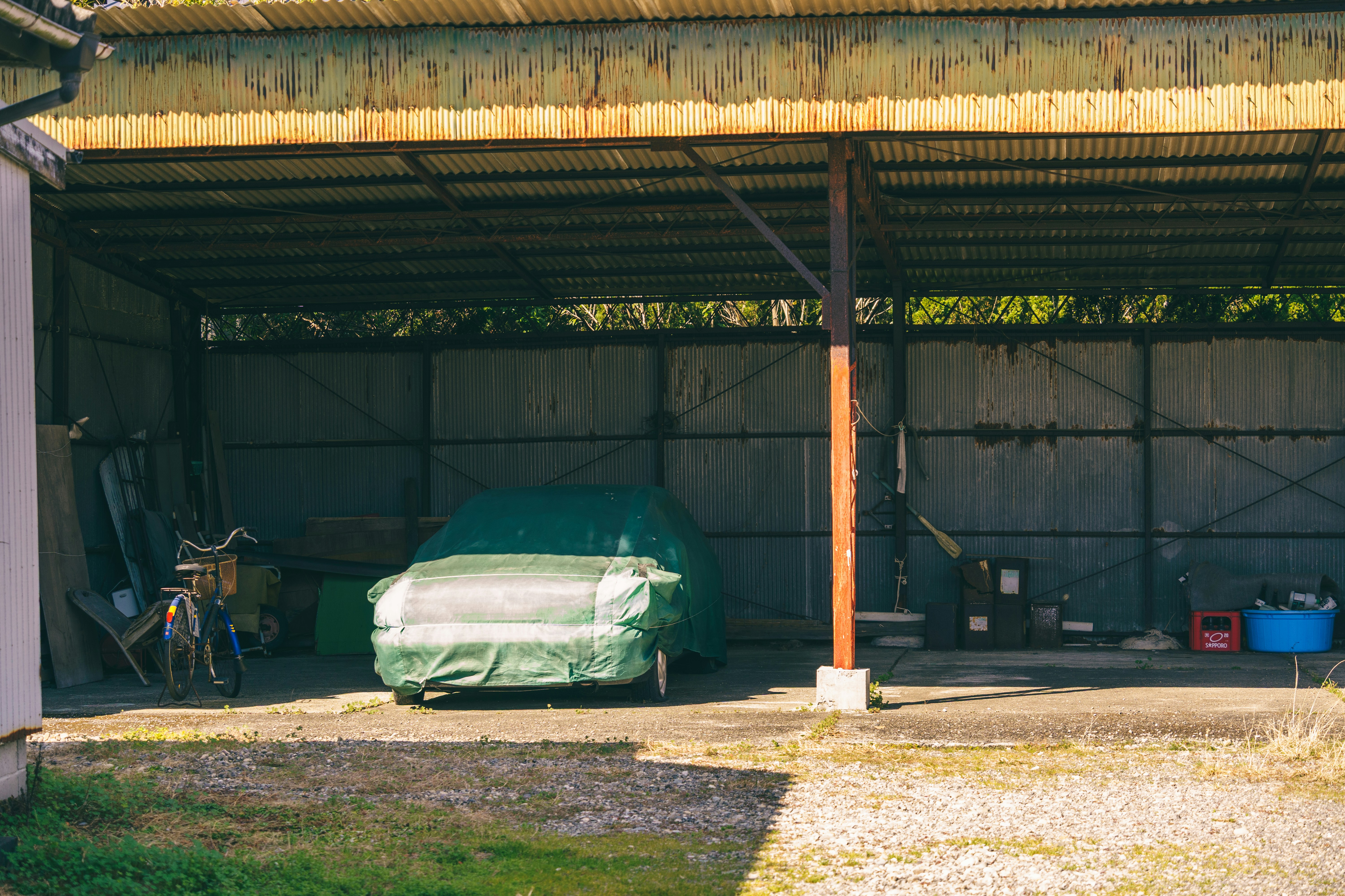 Hidden Car Shelter: A Green-Tarped Car Quietly Guarded Under a Workshop Canopy