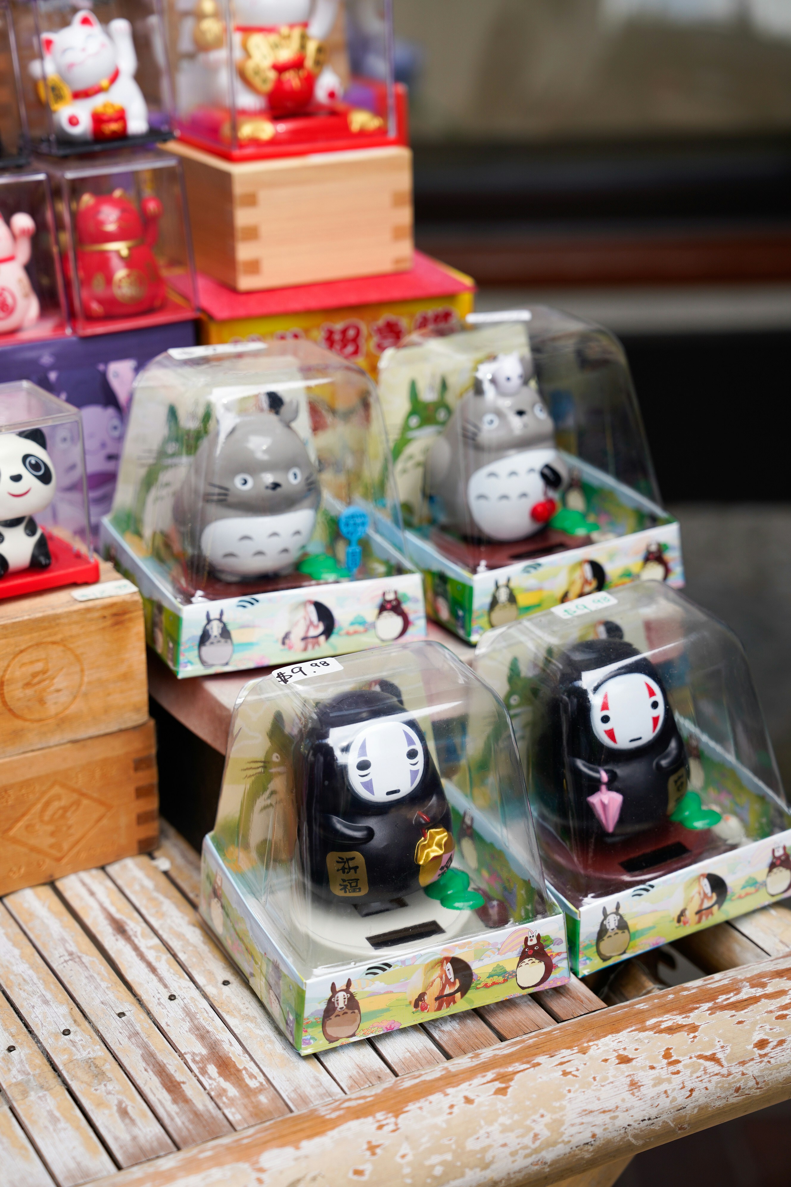 Colorful toy figurines under clear domes are neatly arranged on a wooden display, showcasing various character designs and packaging in a shop setting.