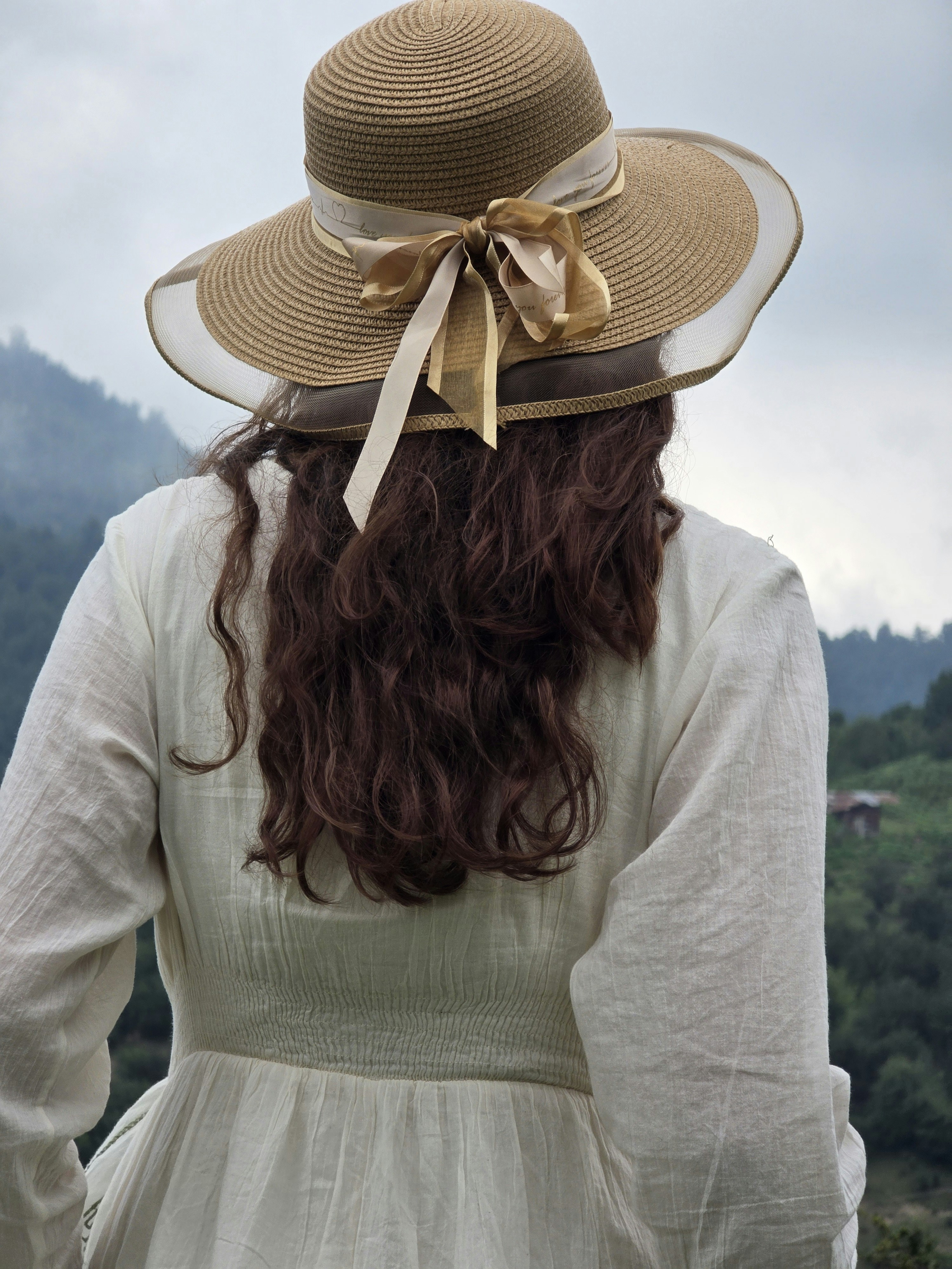 Braid in the breeze: A woman in a sunhat overlooks a misty valley