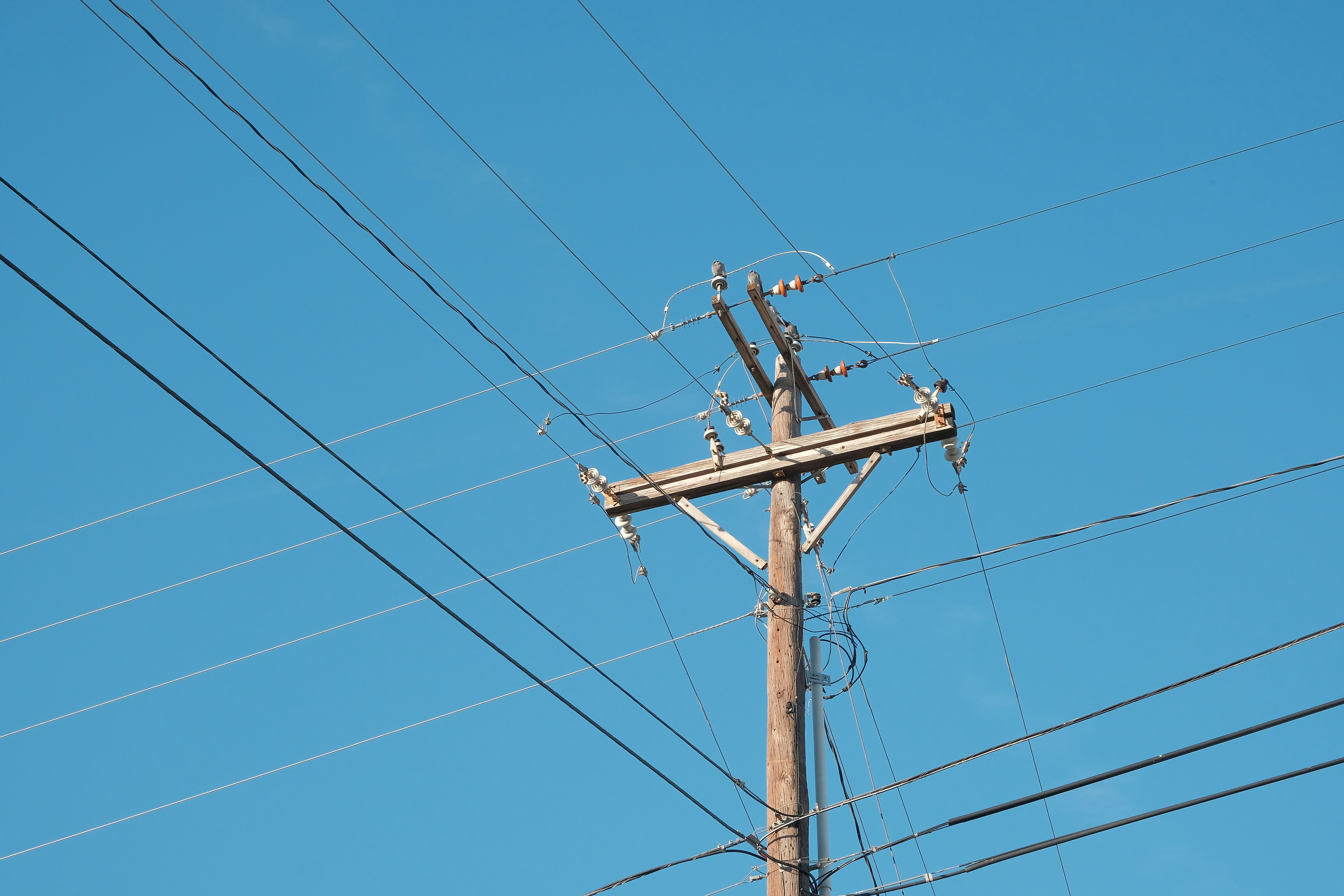 Tall wooden utility pole with cross-arm and multiple power lines set against a clear blue sky; emphasizes infrastructure details. (Logos/illustrations not present.)