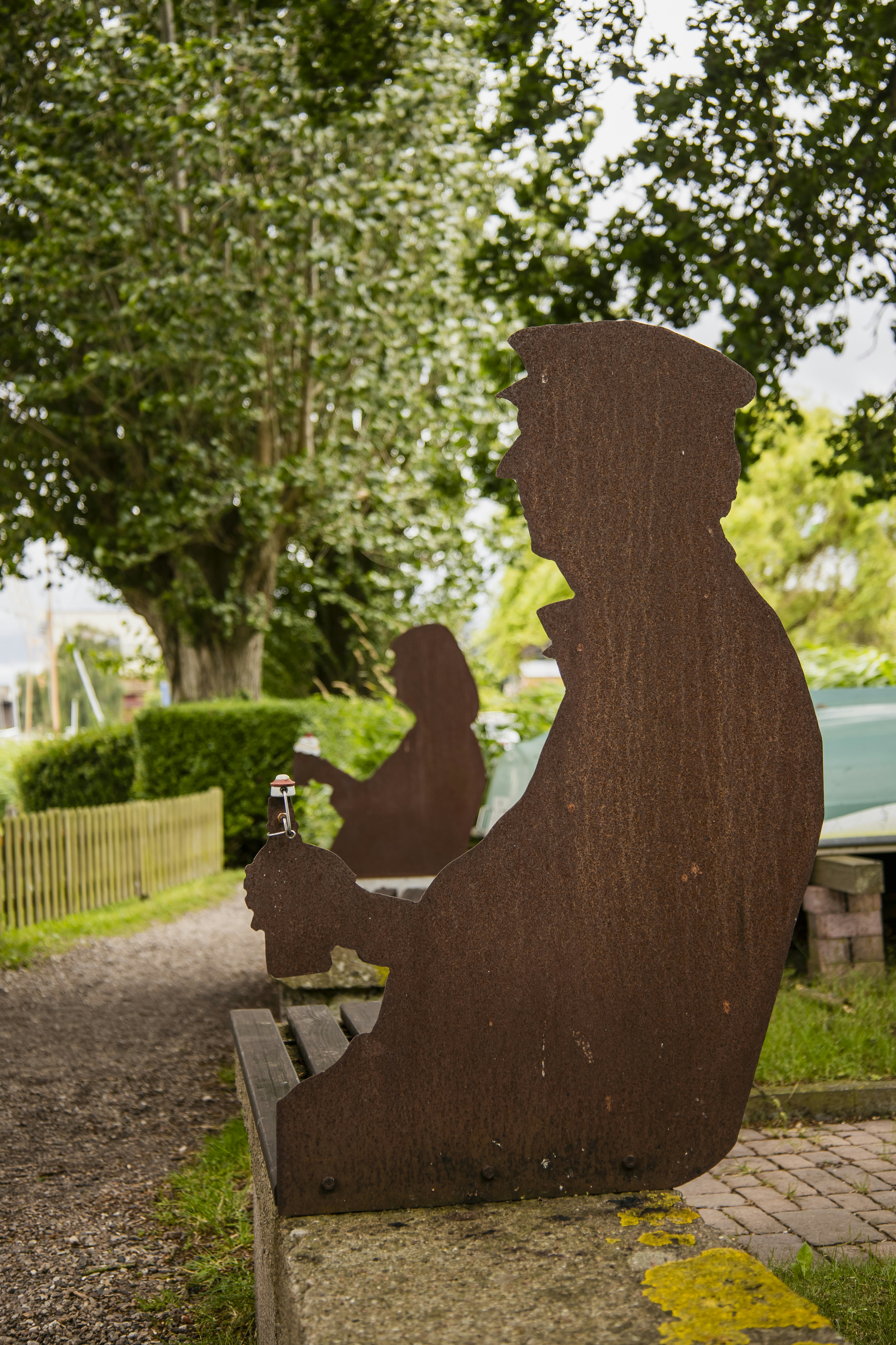 Rusty silhouette of a seated man with a bottle in a park sculpture field