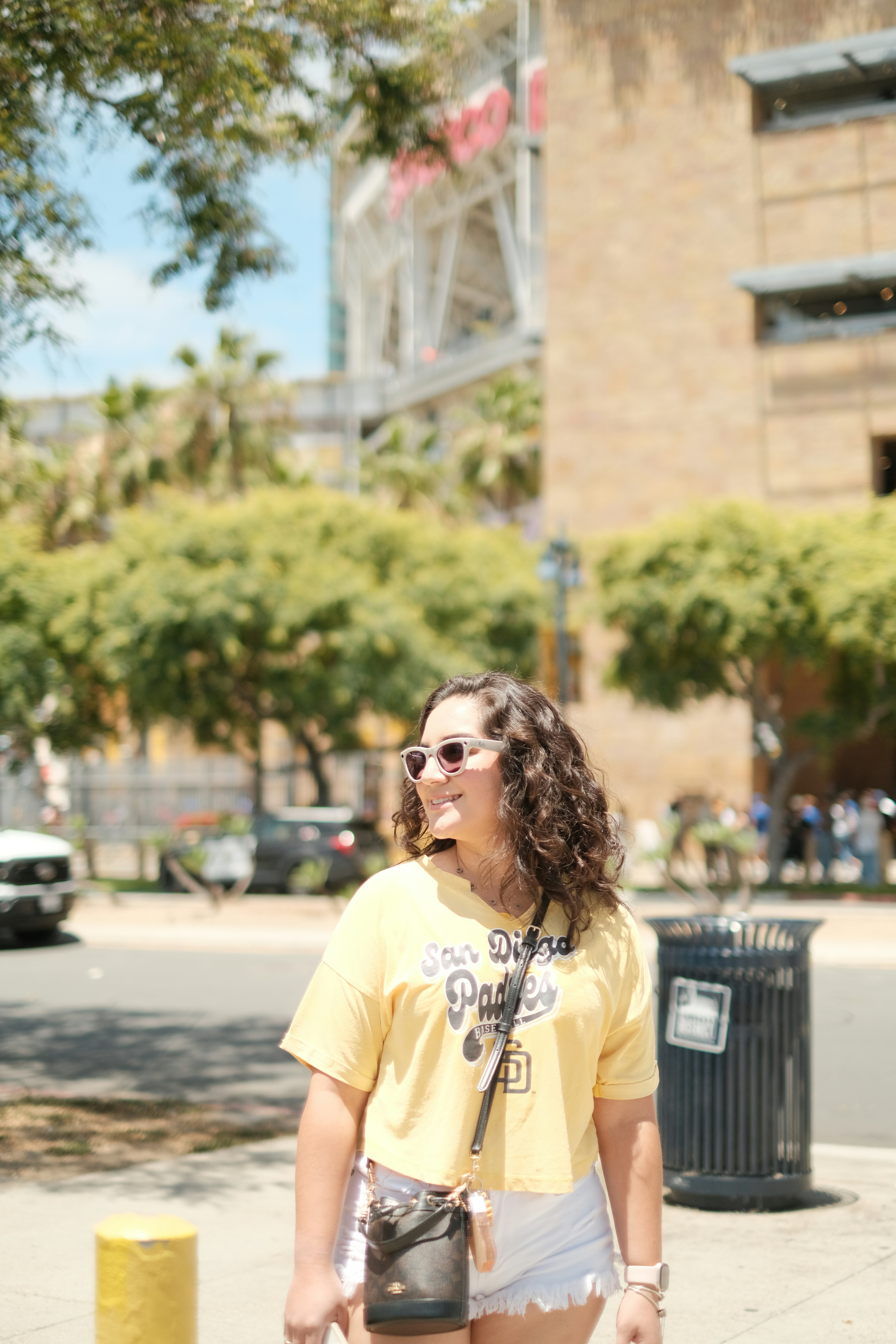 Sunny Street Portrait: A Woman in Yellow T-shirt Walks Past Urban Greenery