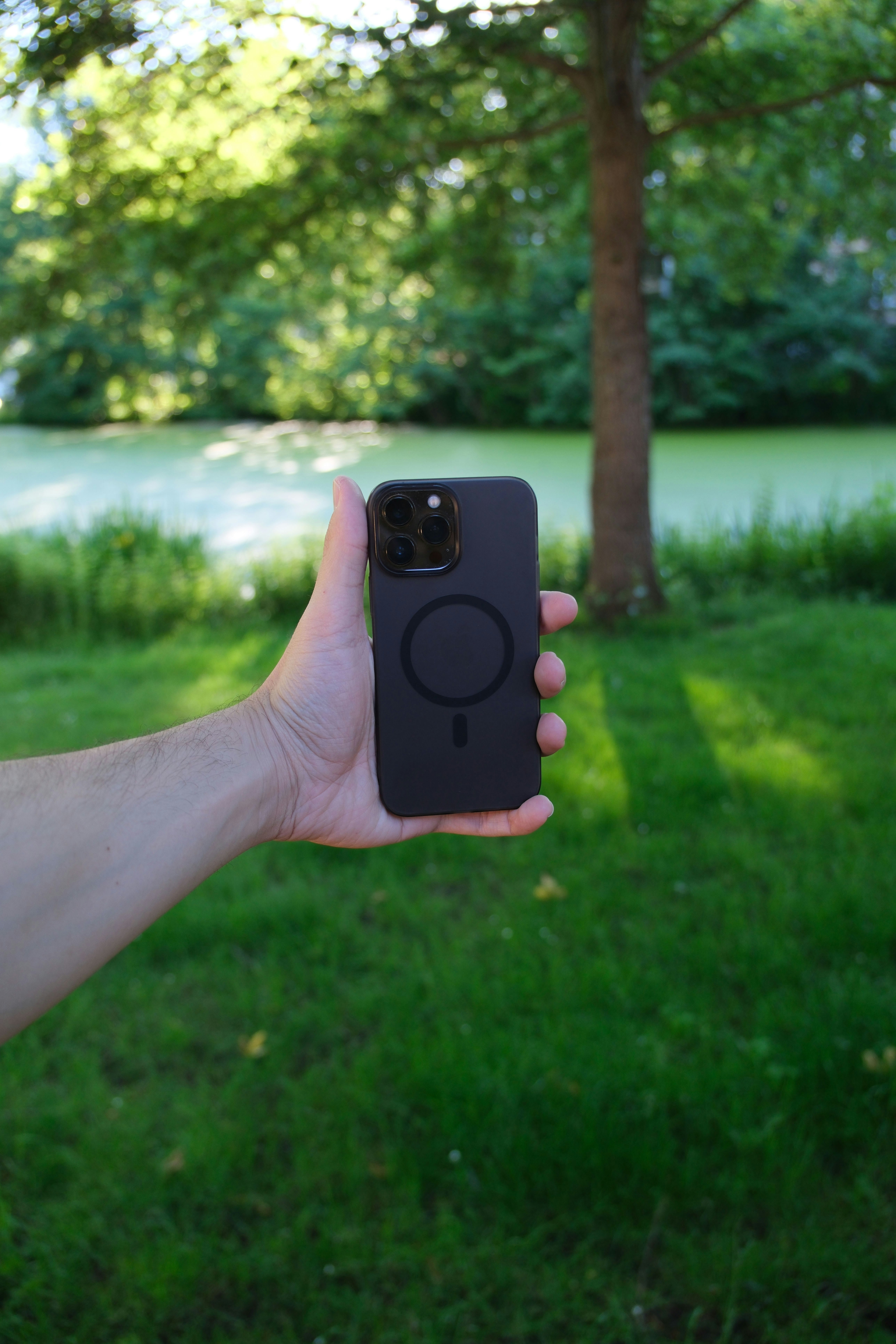 Handheld Moment: A Dark Phone Case Gripped Before a Sunlit Park
