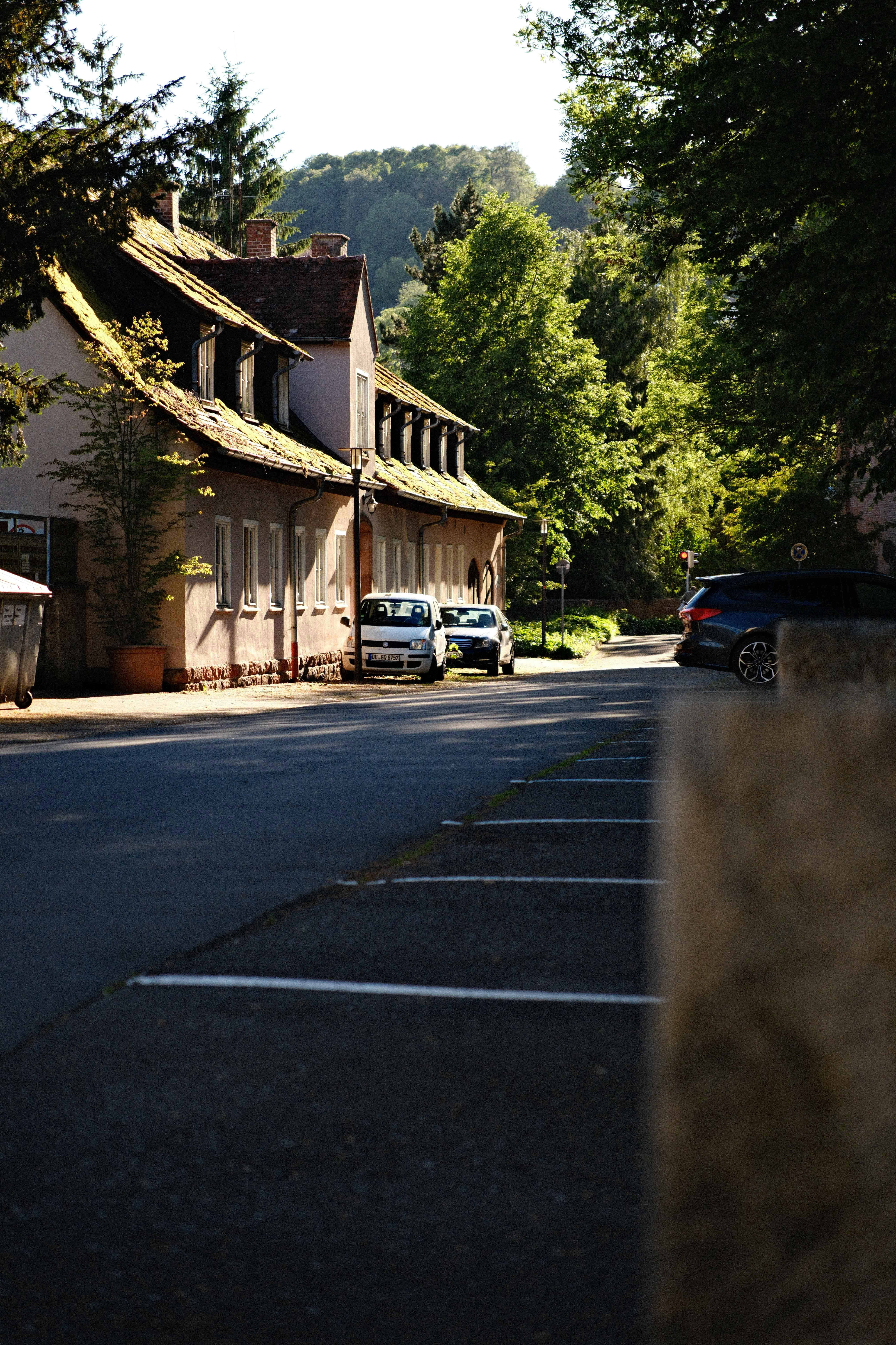 Sunlit street of a European village with parked cars beside a rustic building