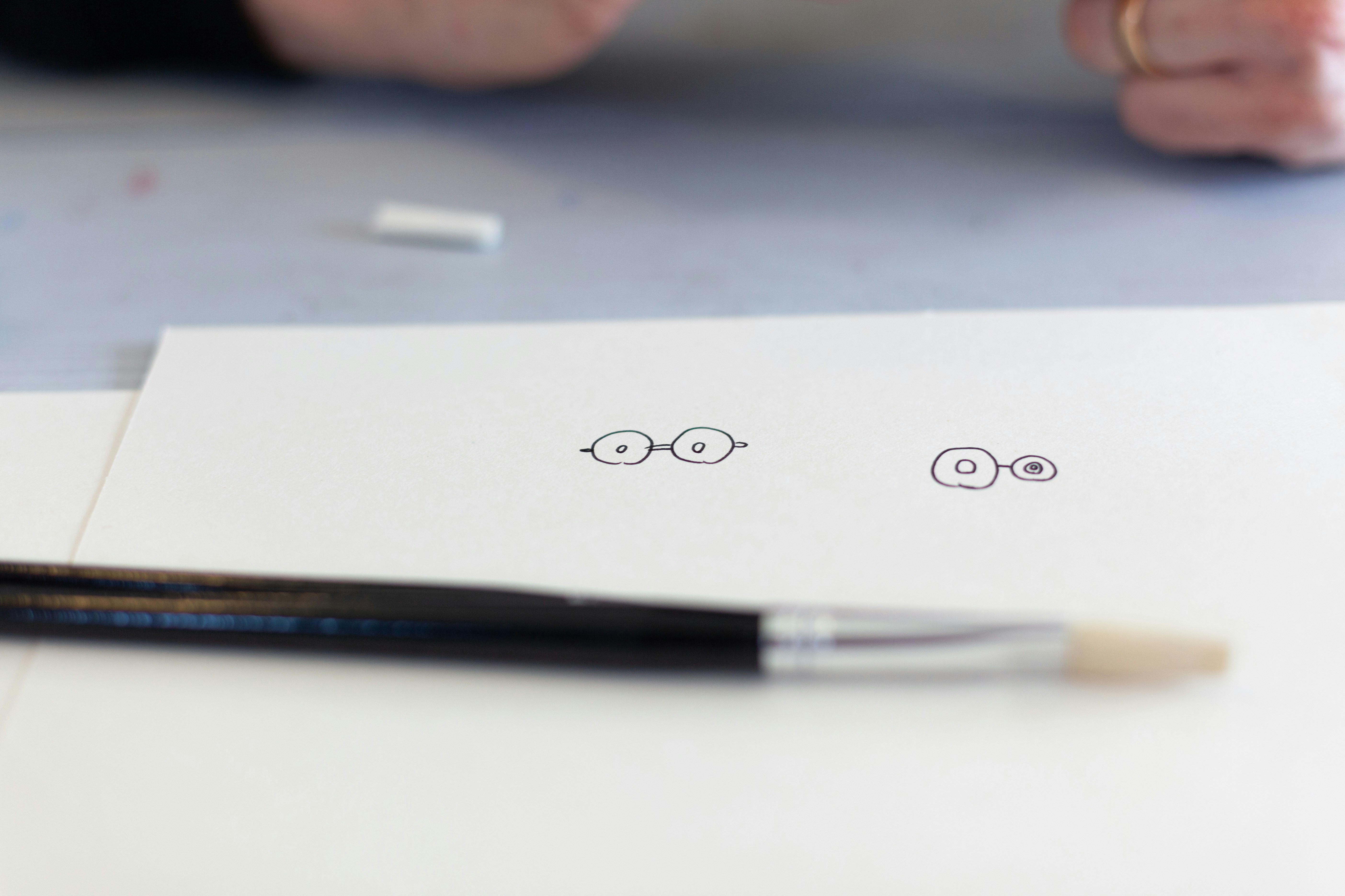 Minimalist sketch of round spectacles on a white sheet with a blurred pen in foreground