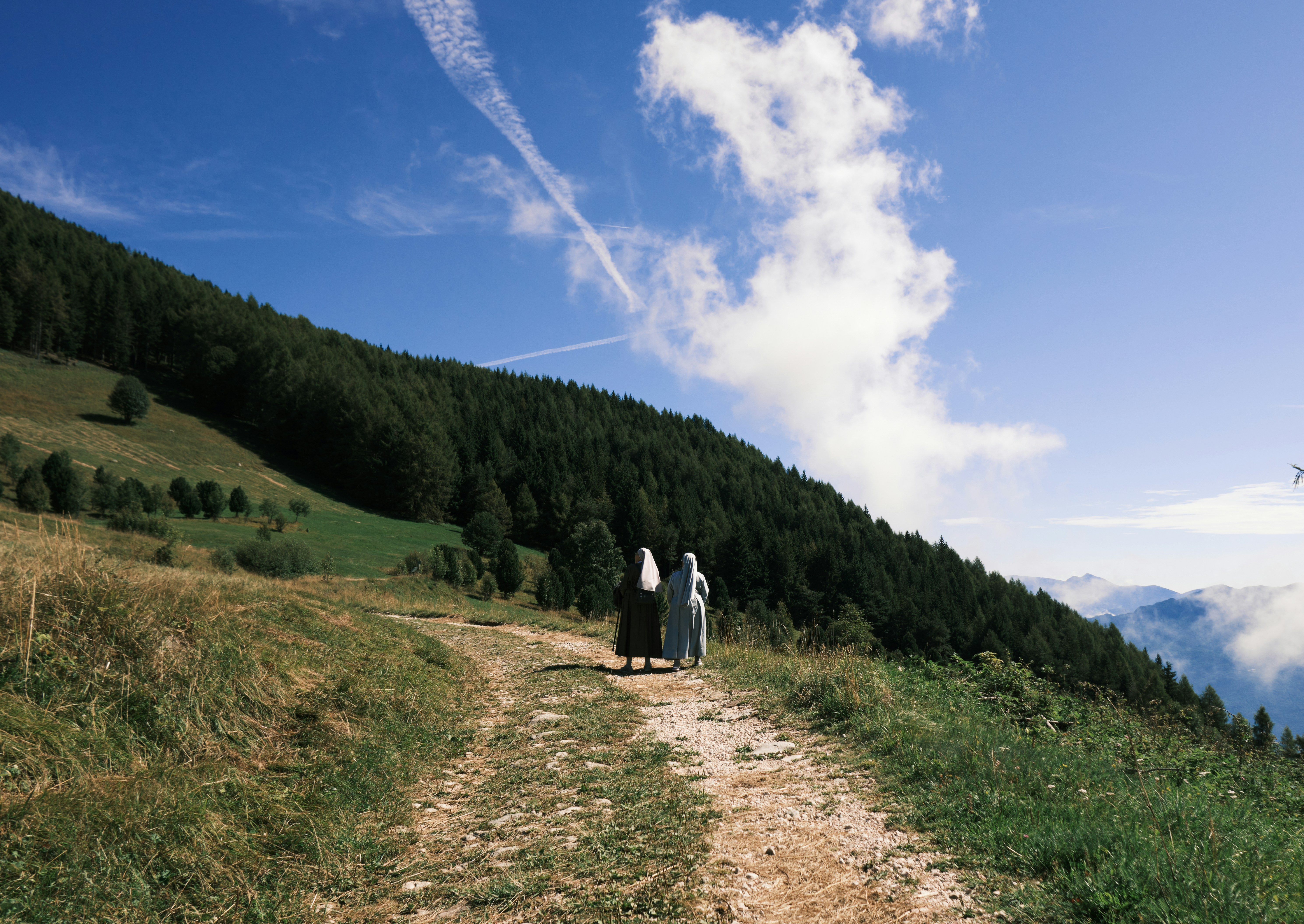 Two hikers on a sunlit mountain path framed by rolling meadows
