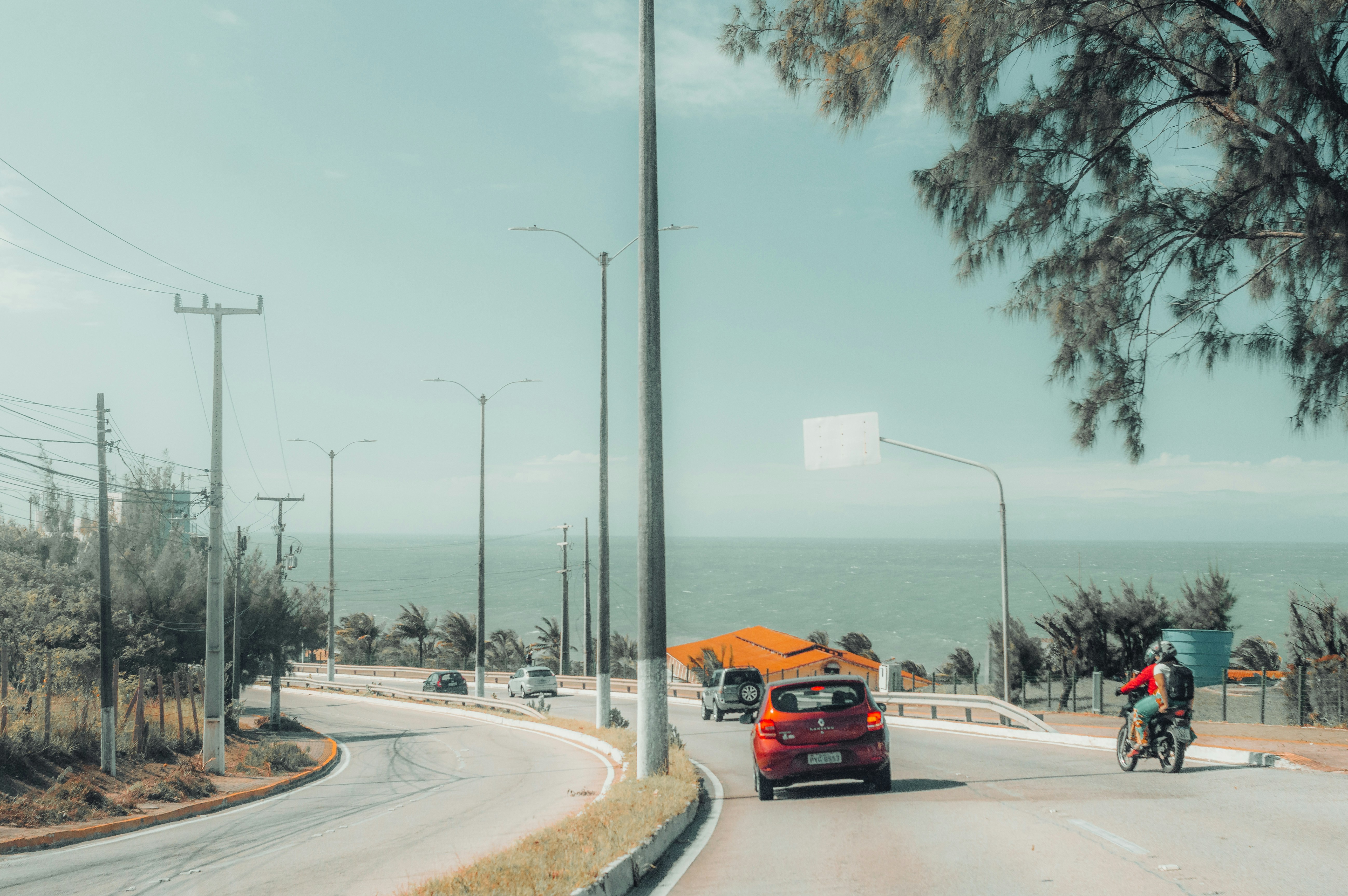 Coastal Curve: A Red Car and a Cyclist on the Ocean Road