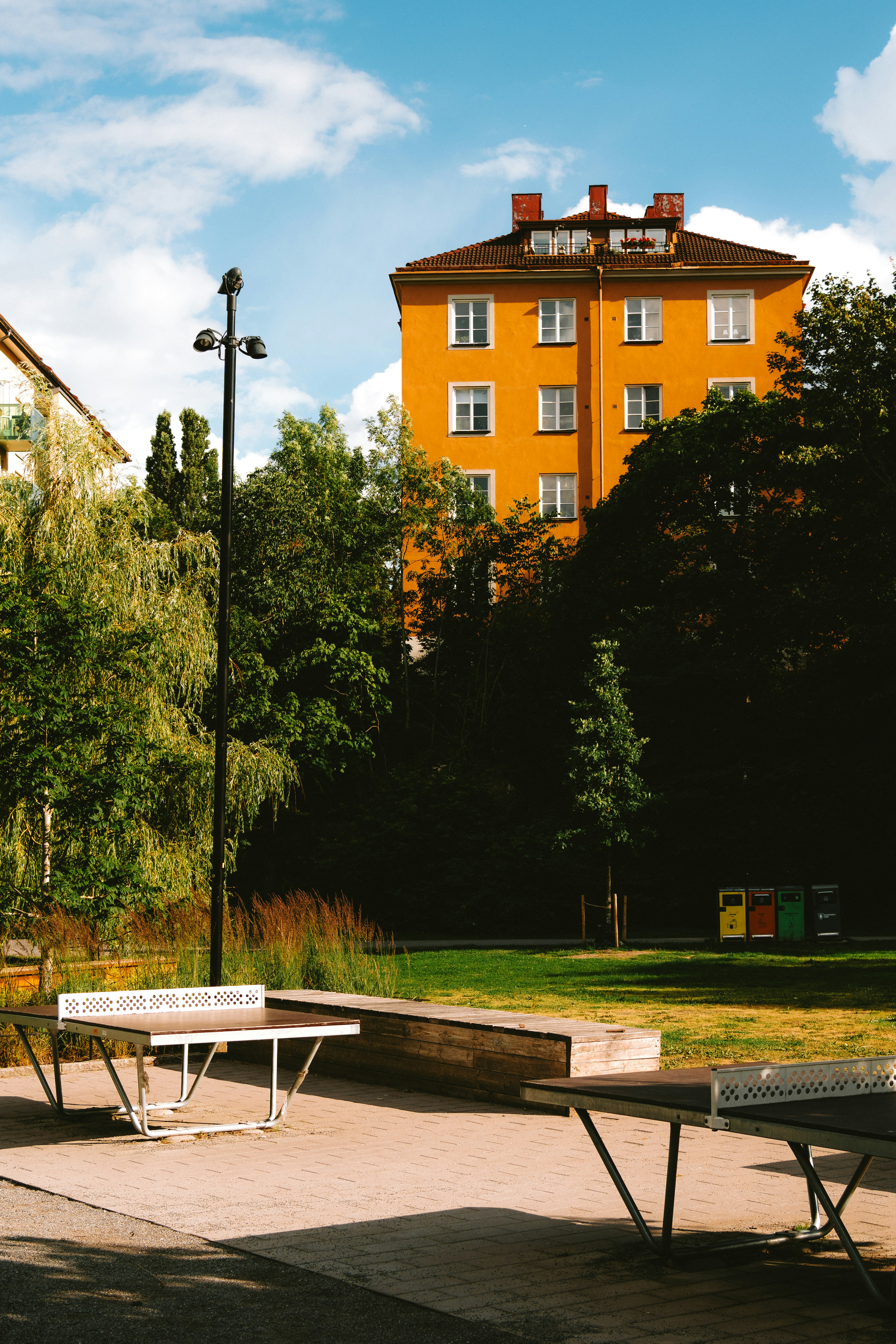 Sunlit Orange Block Towers Over Park with Ping-Pong Tables