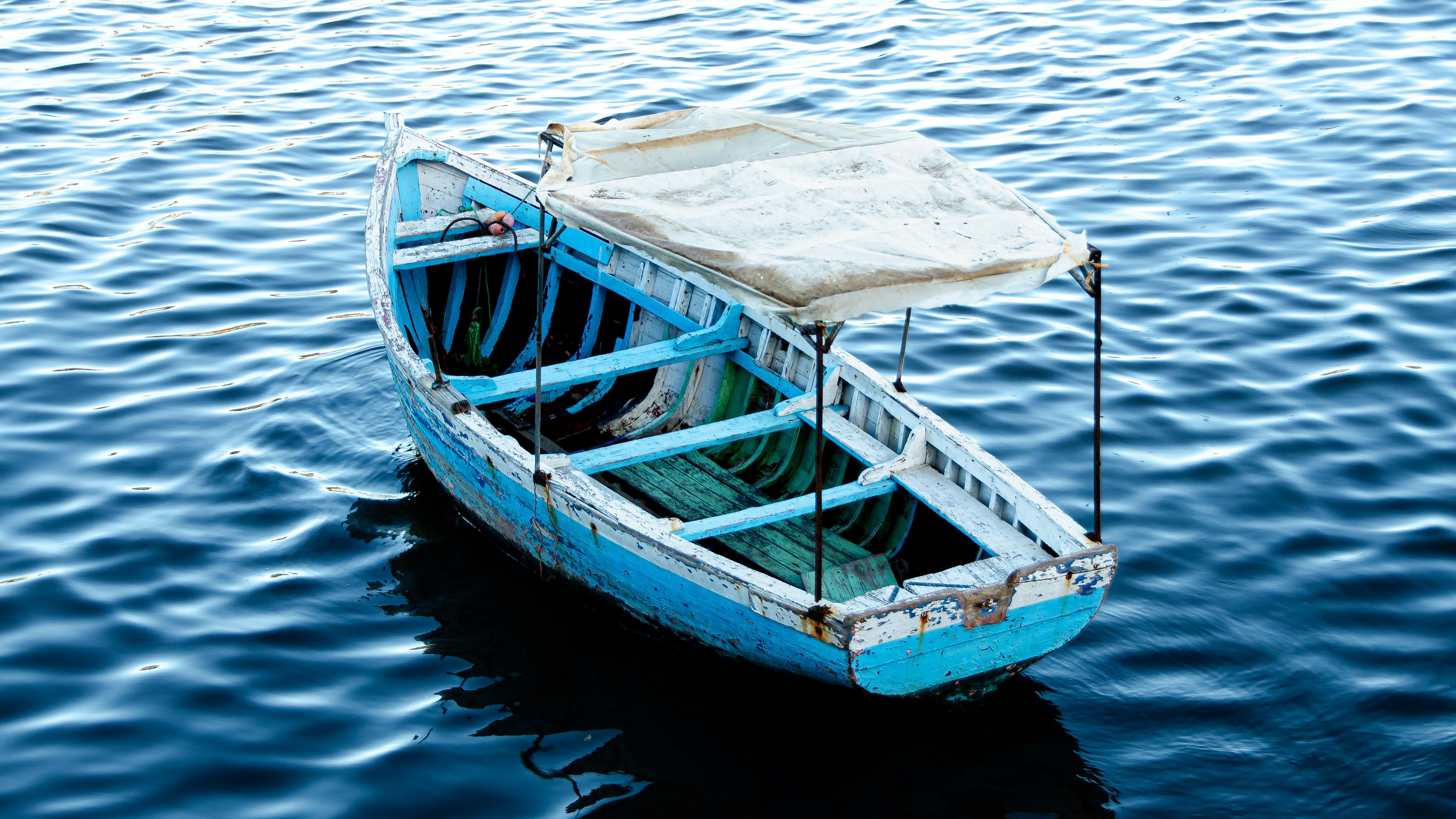 Weathered Blue Rowboat Drifting in Quiet Blue Waters