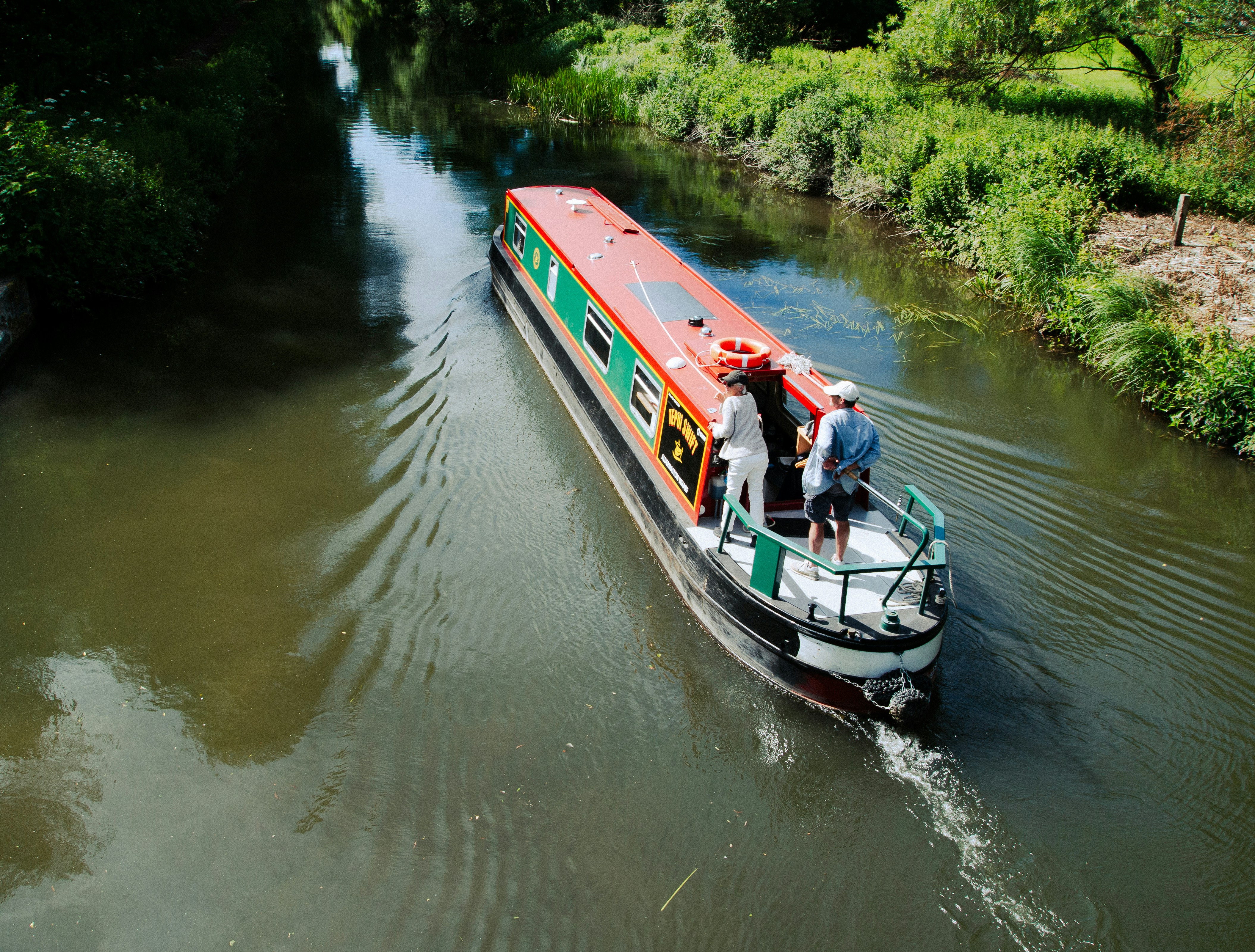 Colorful houseboat gliding along a tranquil canal with lush greenery framing the water.