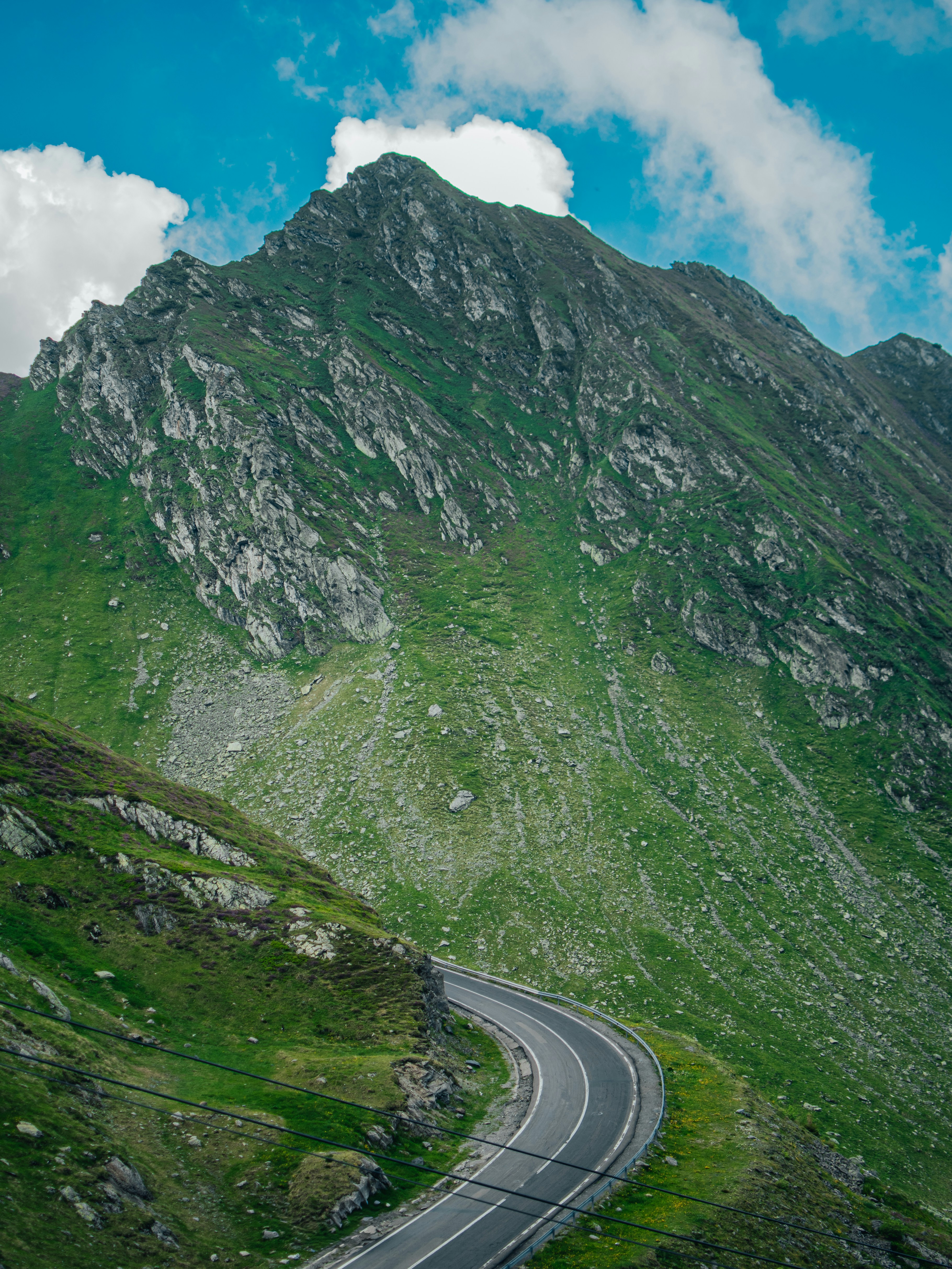 Crest of the Curve: A Winding Road Beside a Verdant Alpine Wall