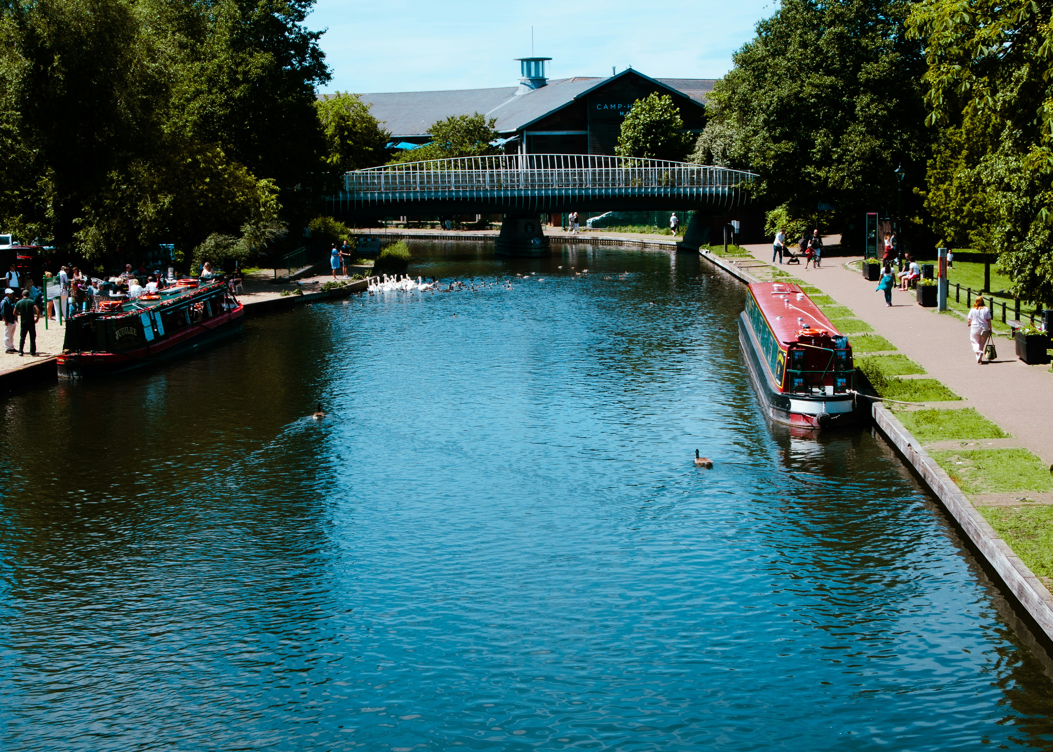 Wide canal scene with a pedestrian bridge spanning the water and boats moored along the banks.