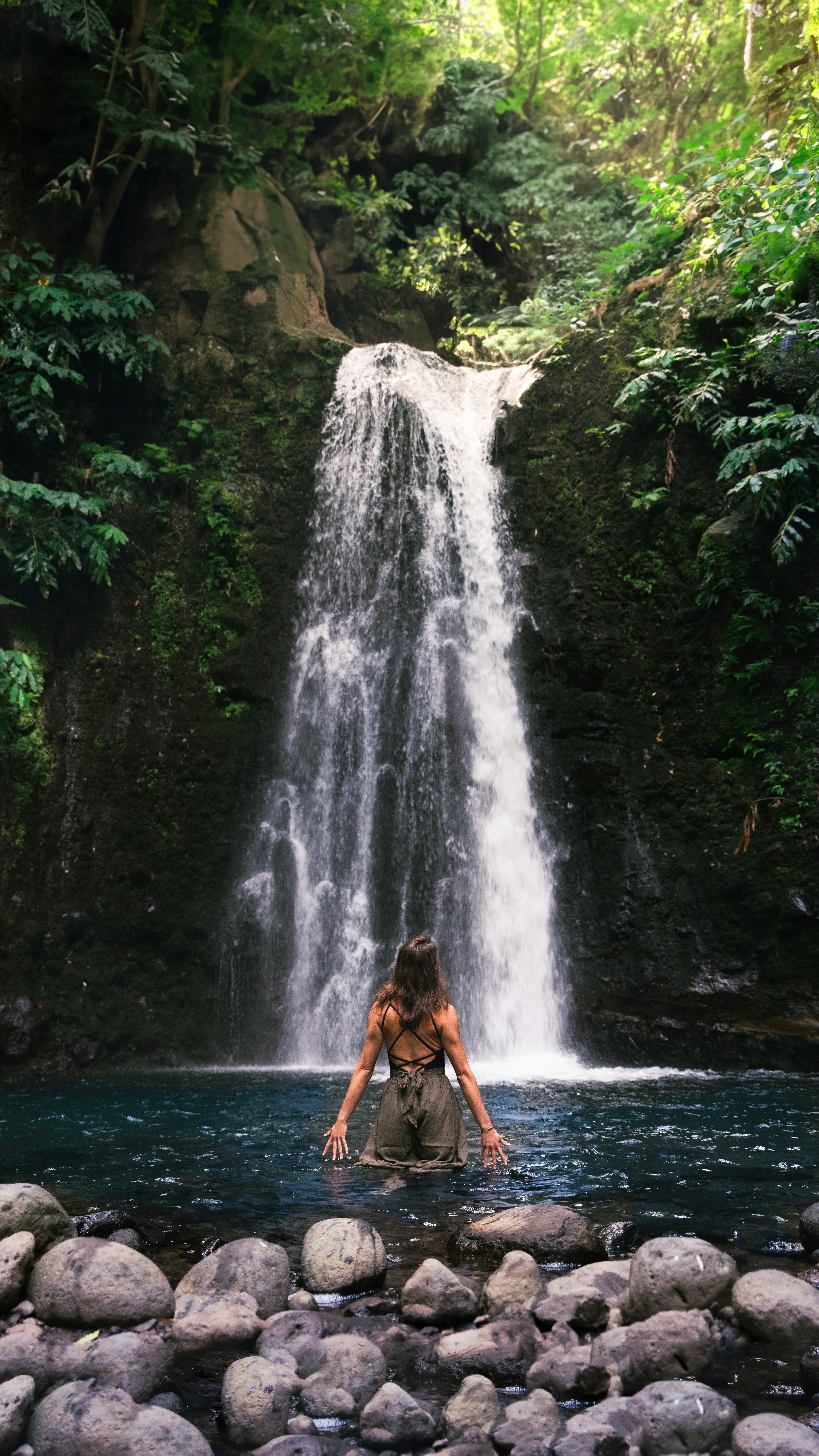 Woman in Waterfront Clearing Beneath a Cascading Forest waterfall