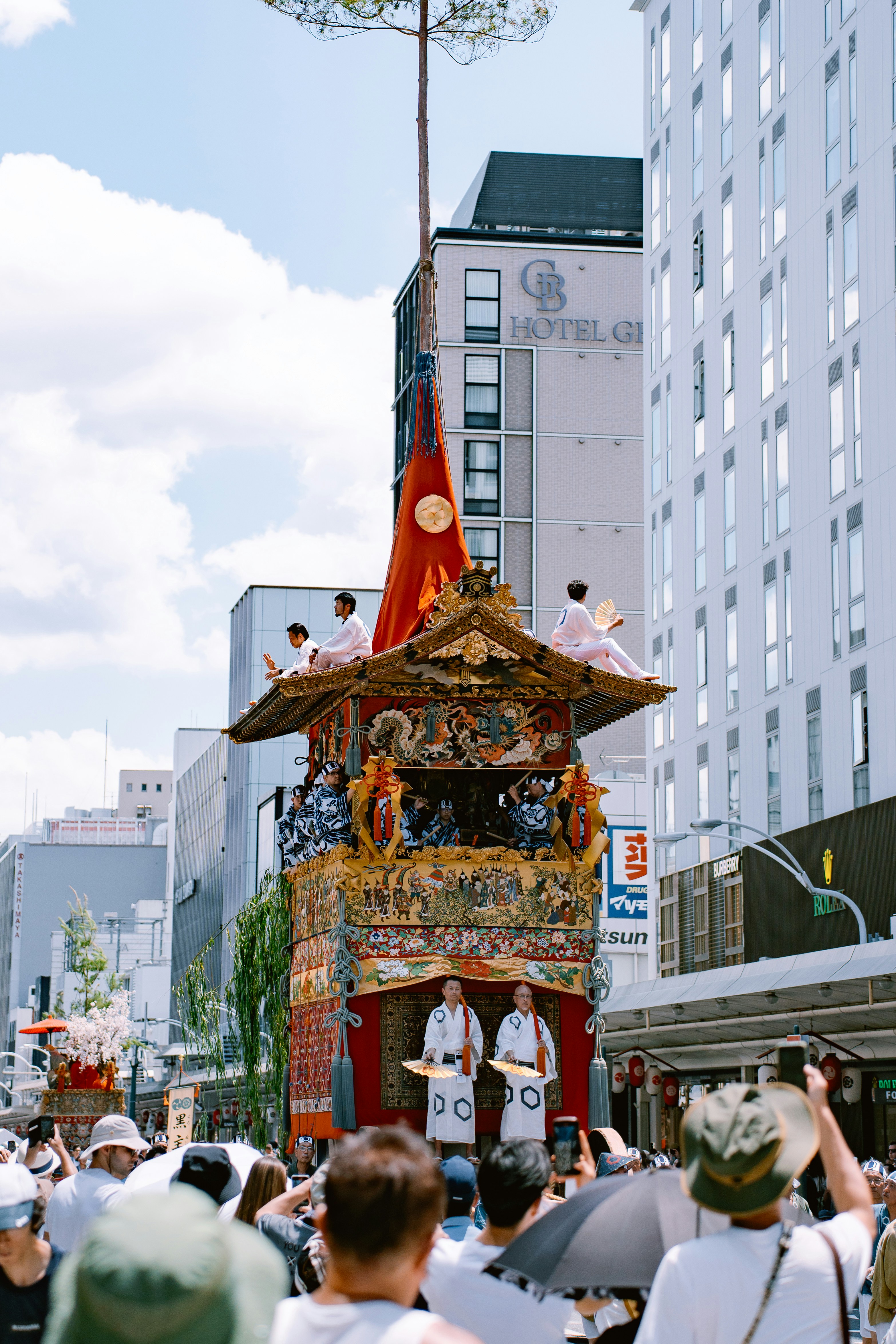 Ornate festival float rides through a city canyon under bright noon skies