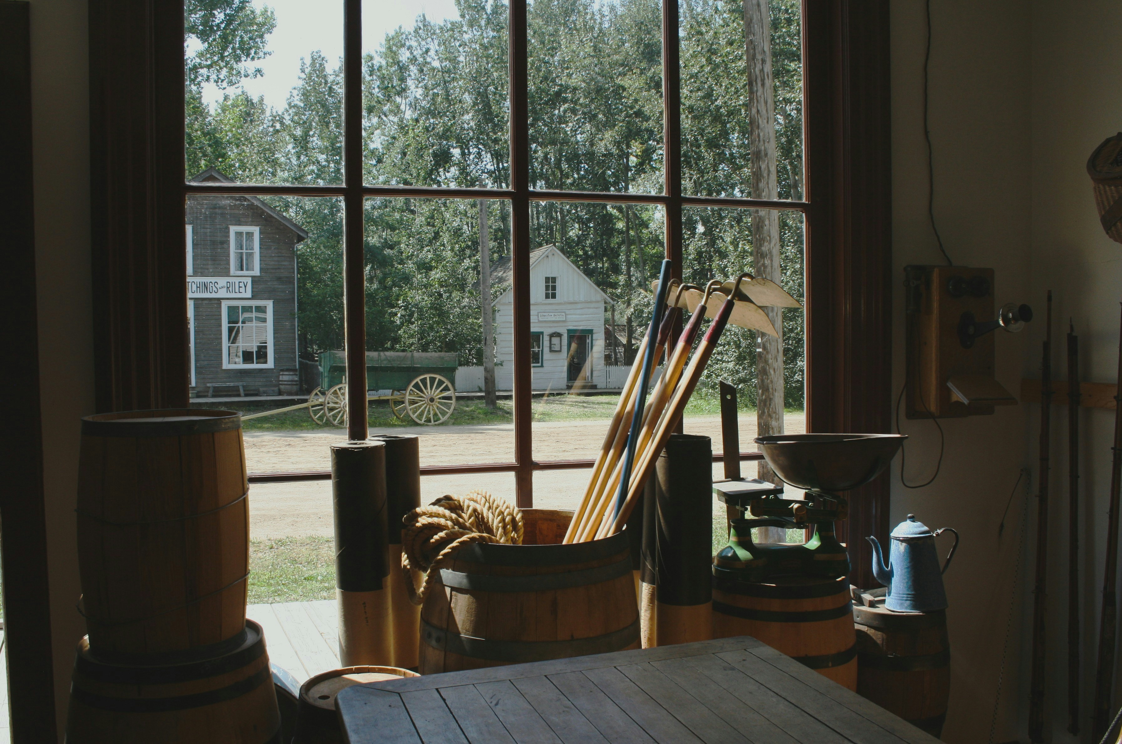 Sunlit Workshop Window: Tools and Oat Baskets Framing a Quiet Farmyard