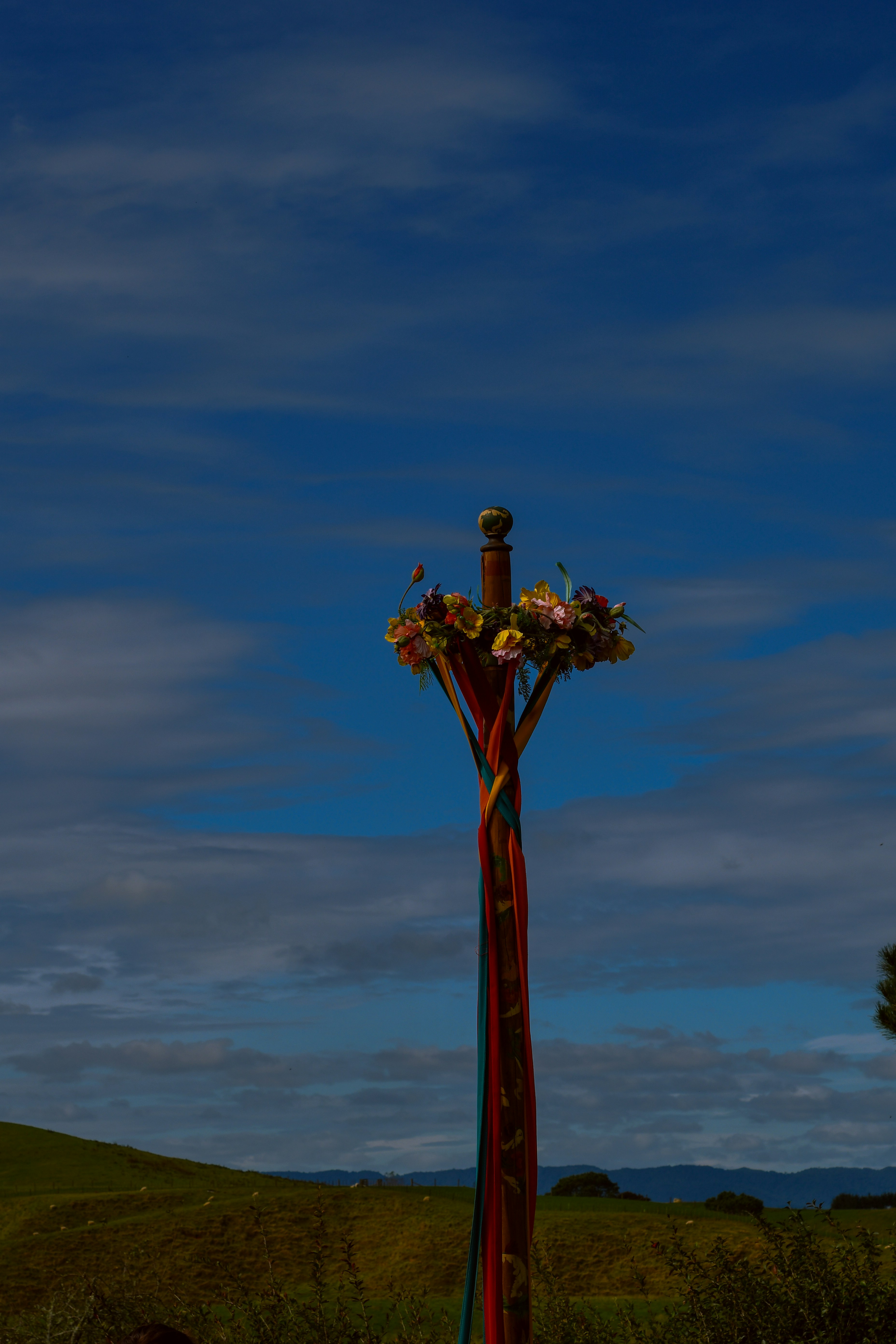 Ritual Post at Dusk: A Floral Cross atop a Painted Pole