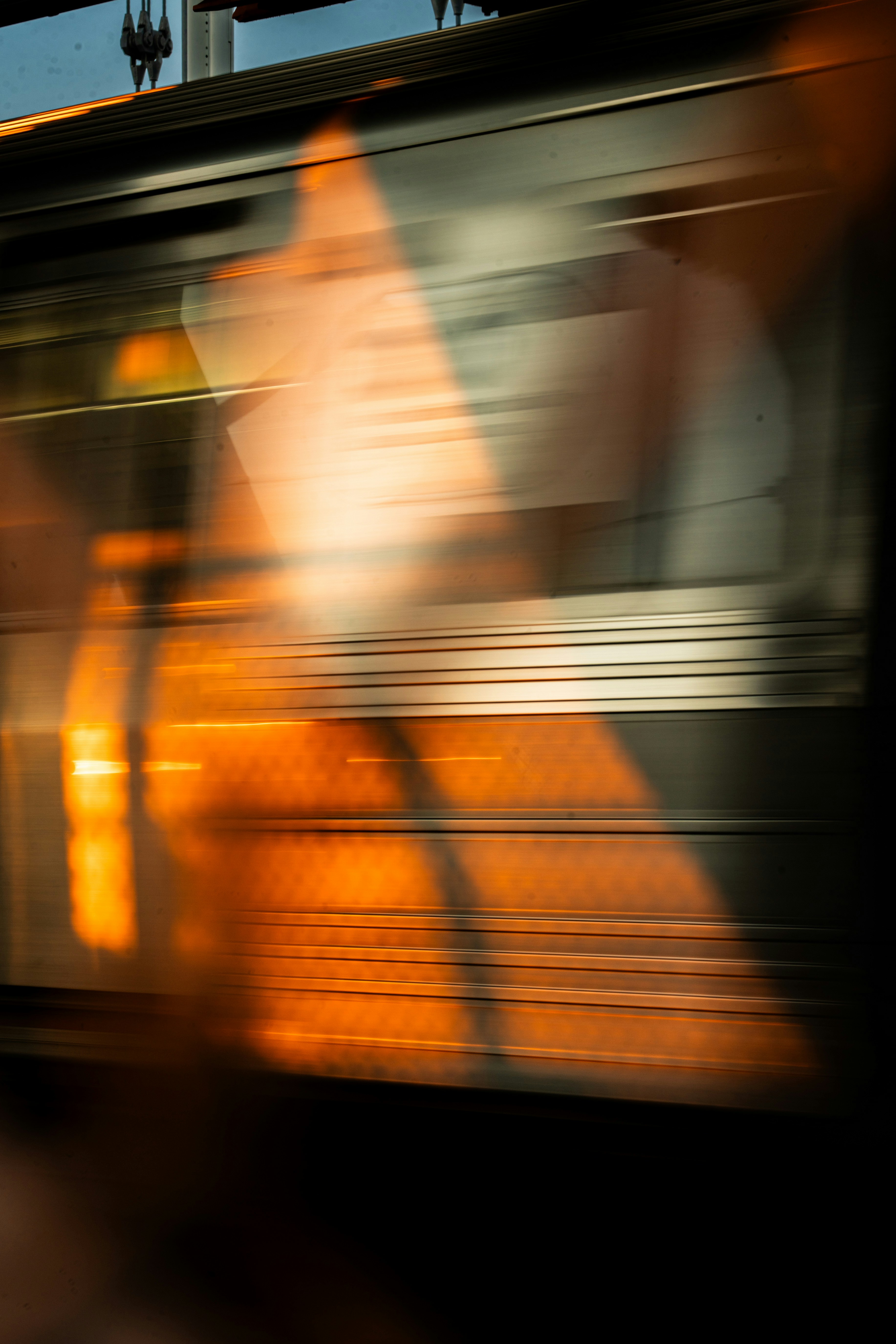 A blurred train car streaks across the frame, its orange glow and metallic panels captured in motion. The image emphasizes speed and light as the subject dissolves into soft, luminous bands.