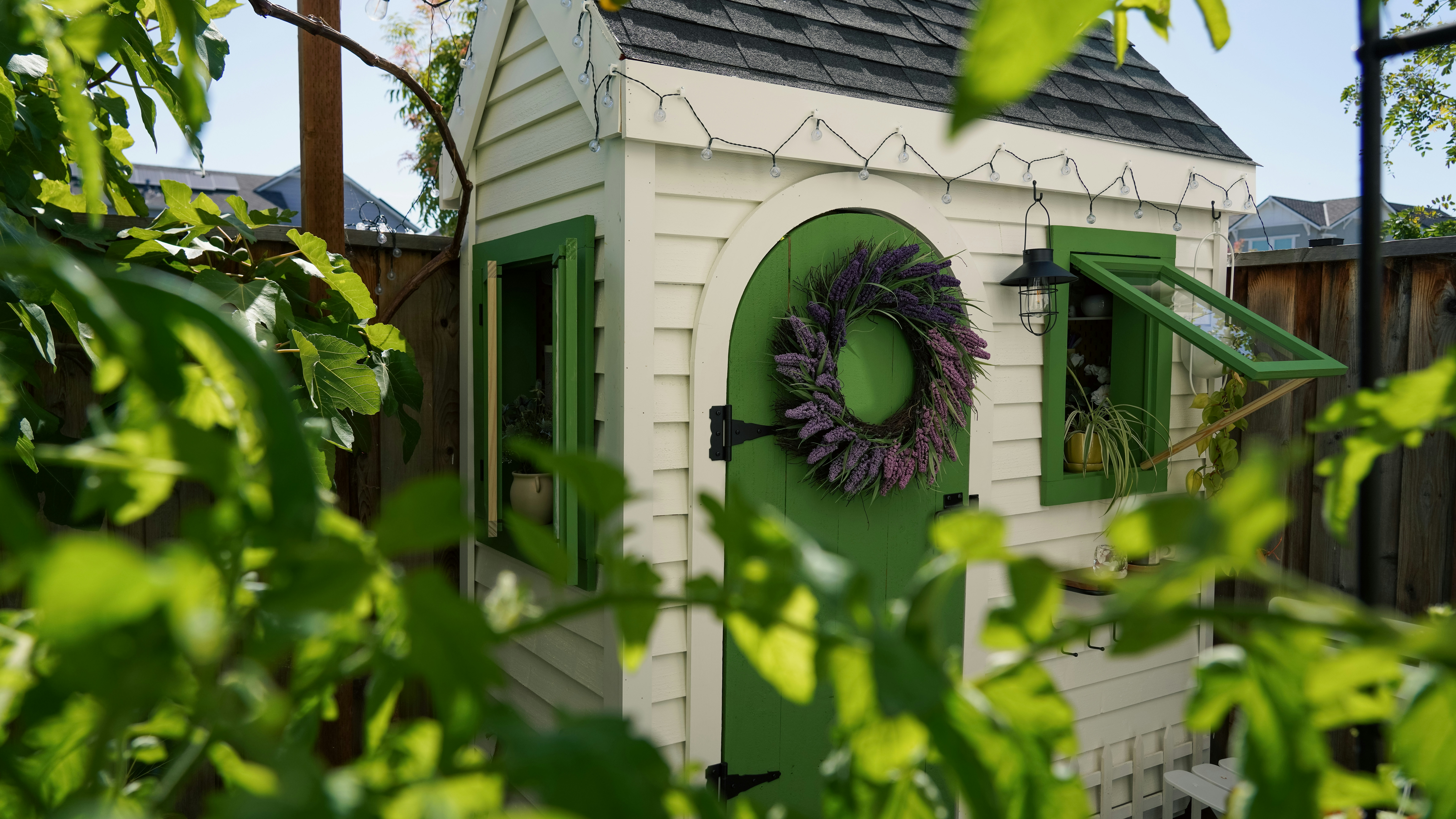 Whimsical Garden Shed with Purple Wreath Amid Green Foliage