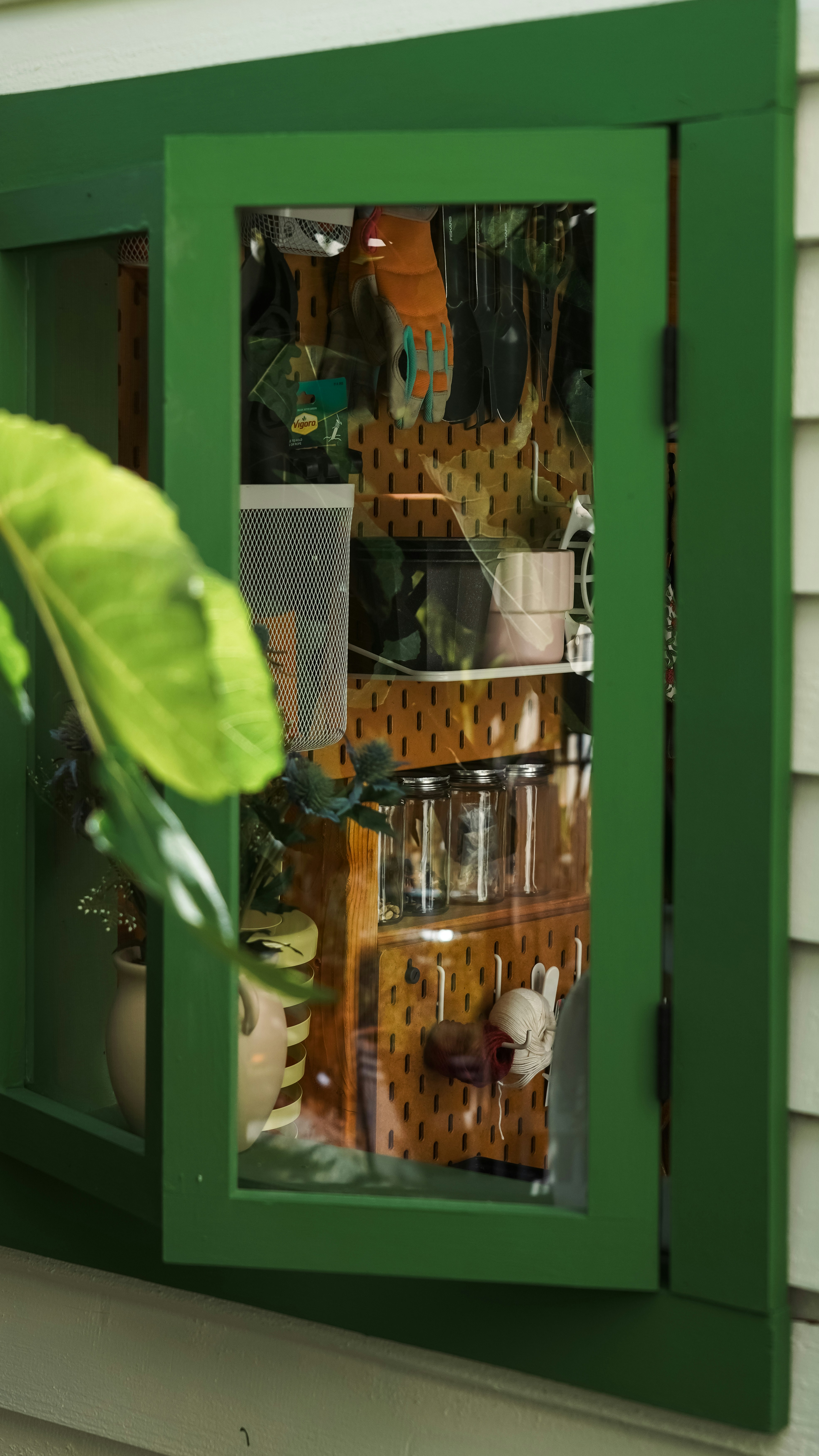 Green cabinet window reveal: a busy pegboard of tools reflected in glass