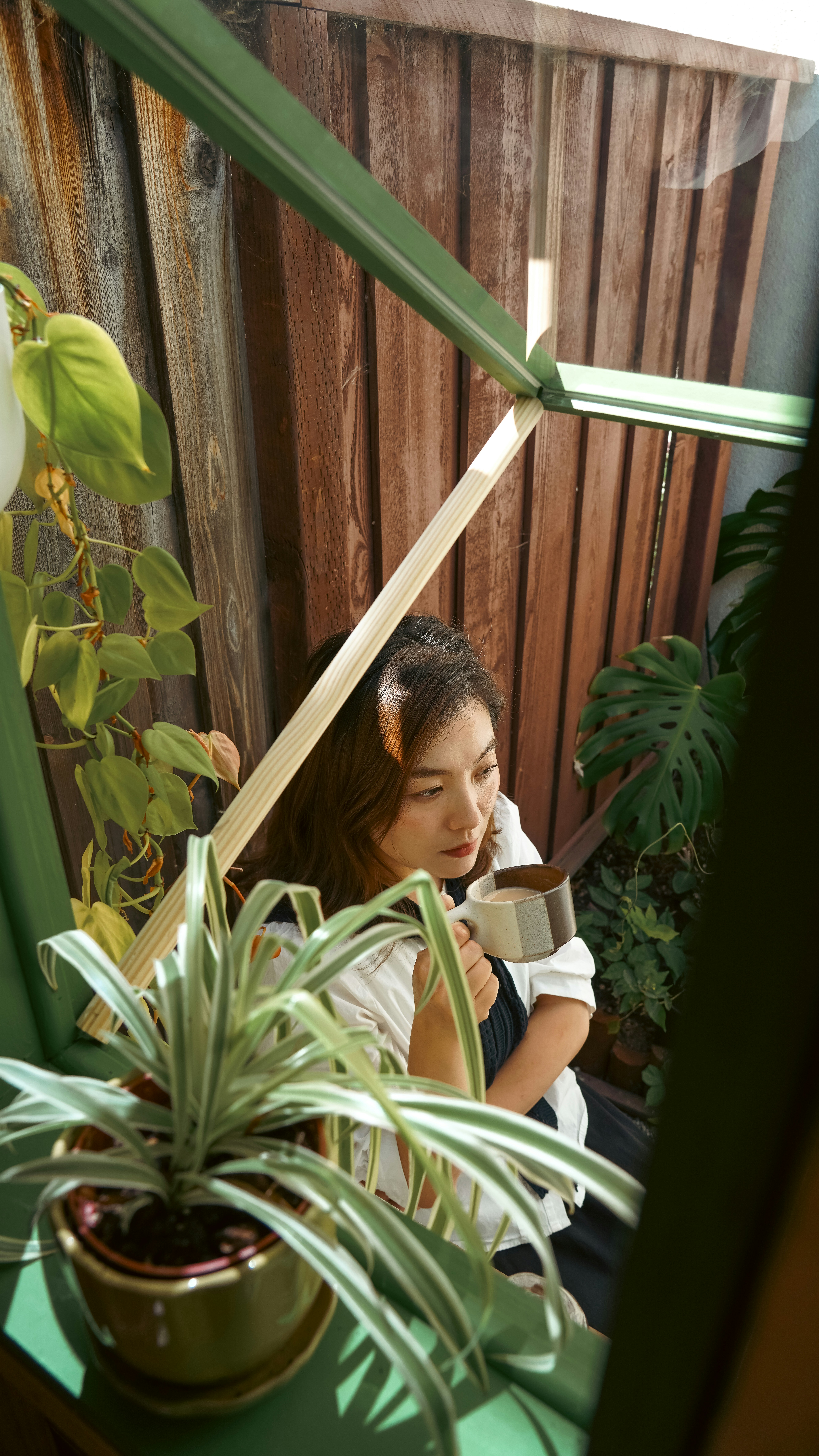 Windowed Quiet: A Woman Sipping Tea Amid Indoor Greenery