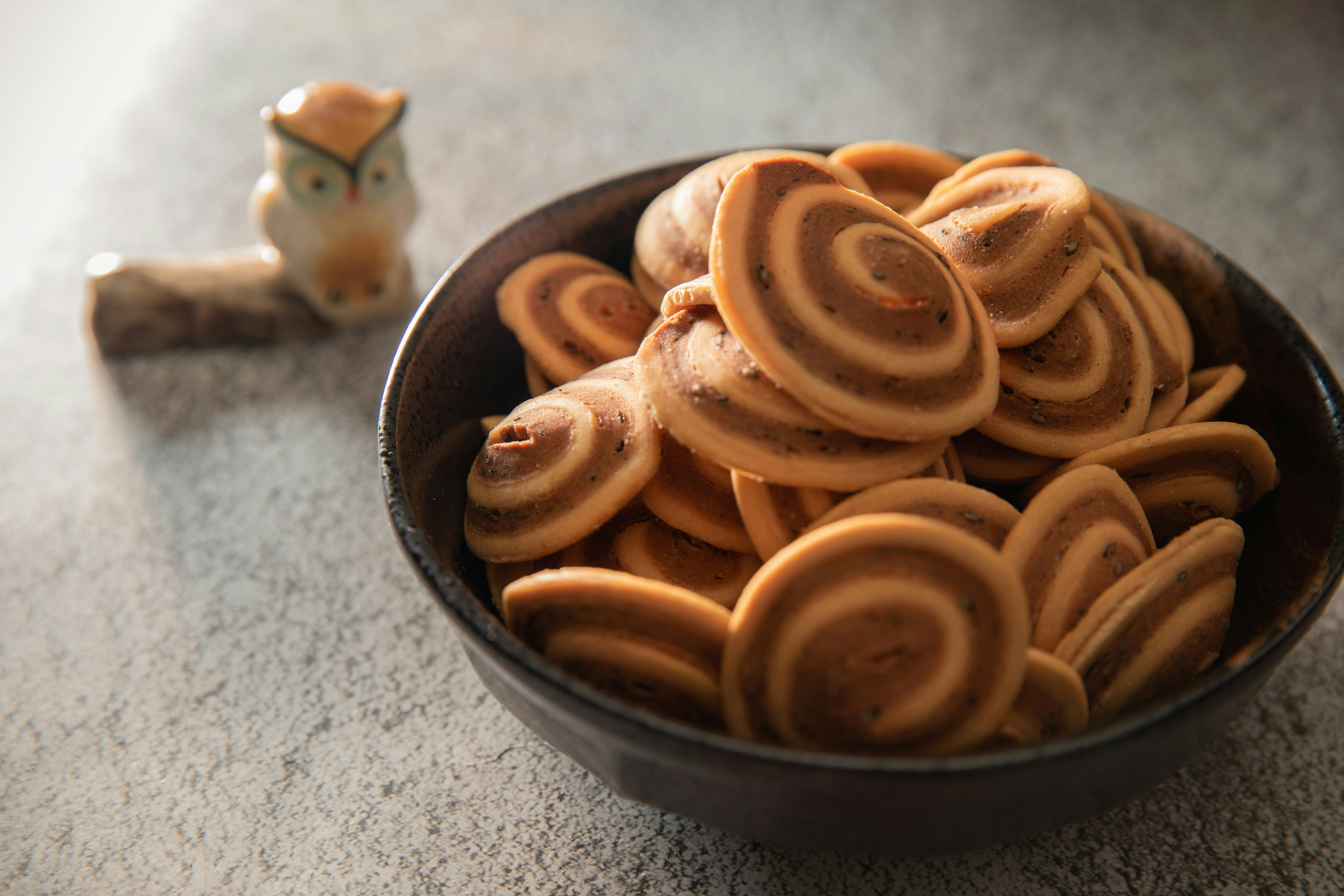 Swirled cookies in a dark ceramic bowl with a tiny owl figurine in the background