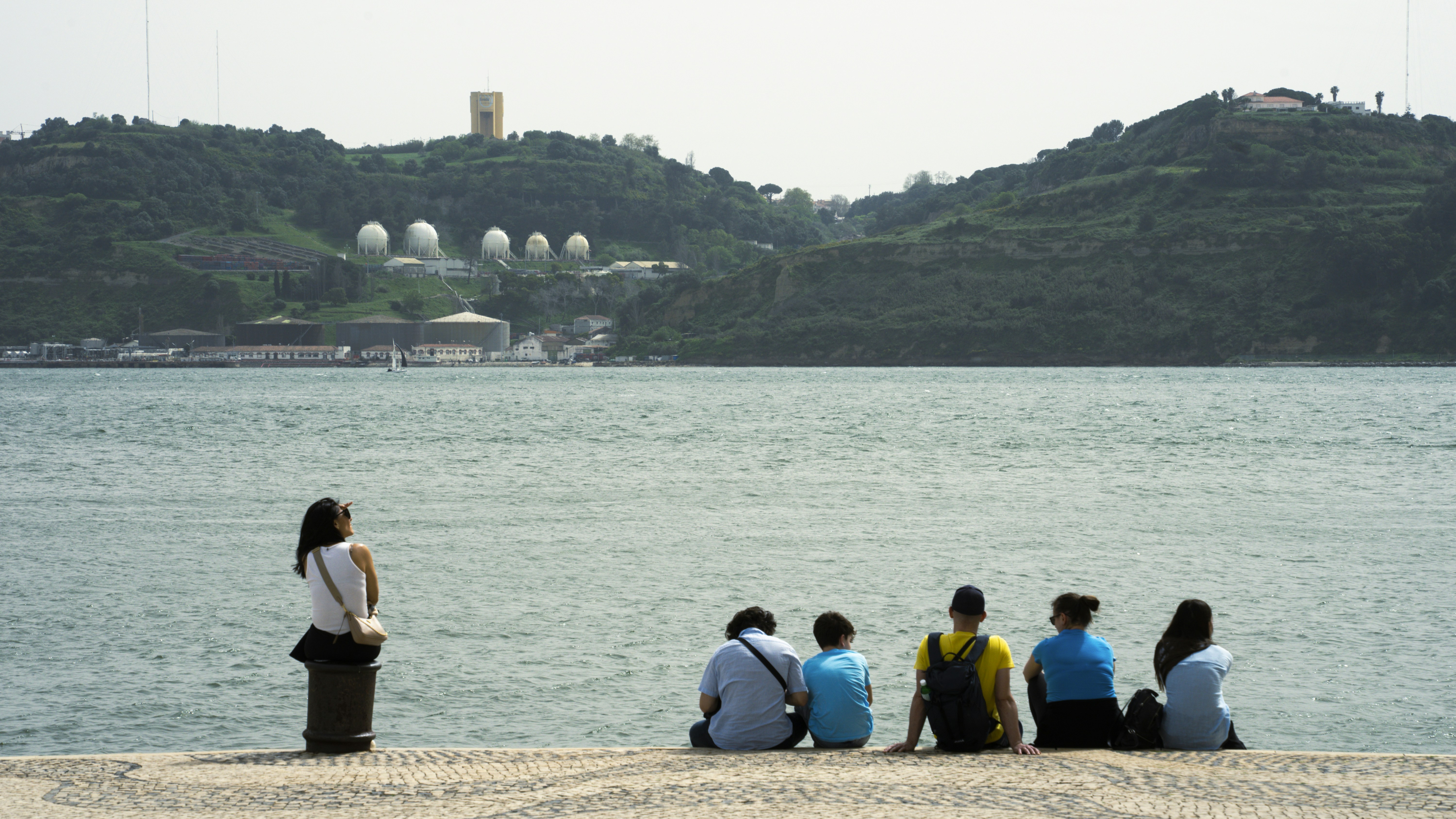 Couple of onlookers at the harbor edge with distant hills