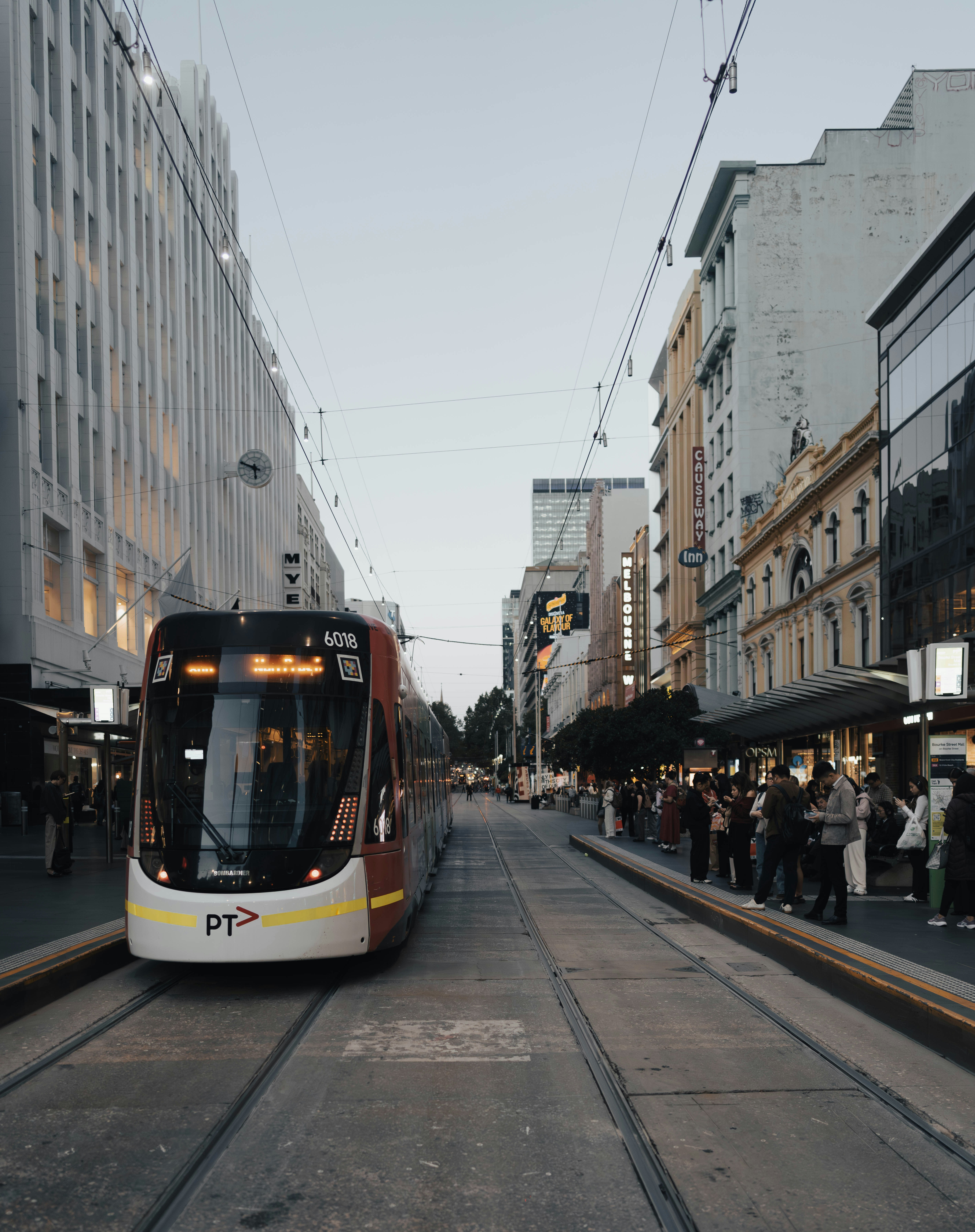 Red tram on tracks in a bustling urban street.