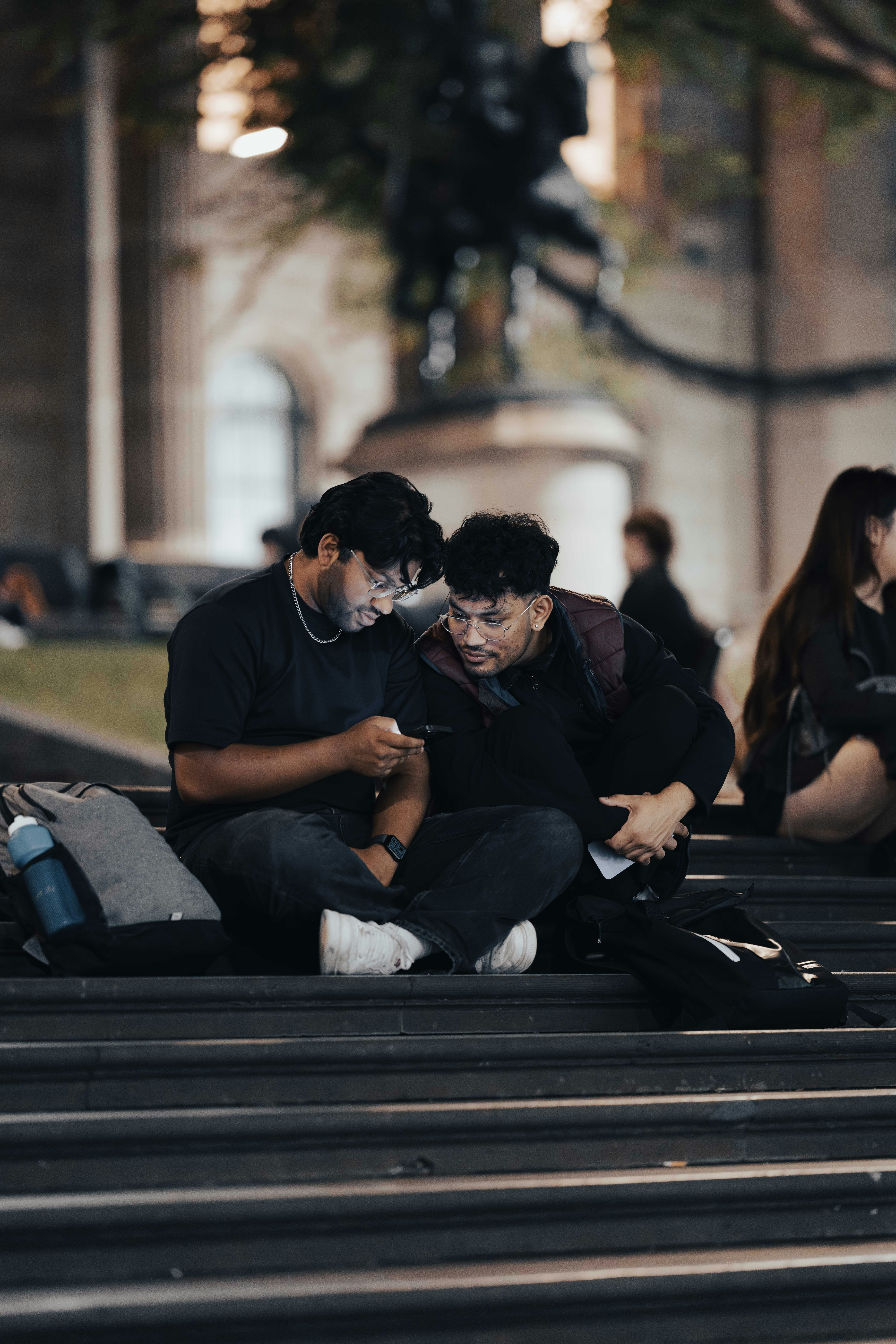 Two Friends on a Bench: Shared Glimpse Over a Phone in a City Square