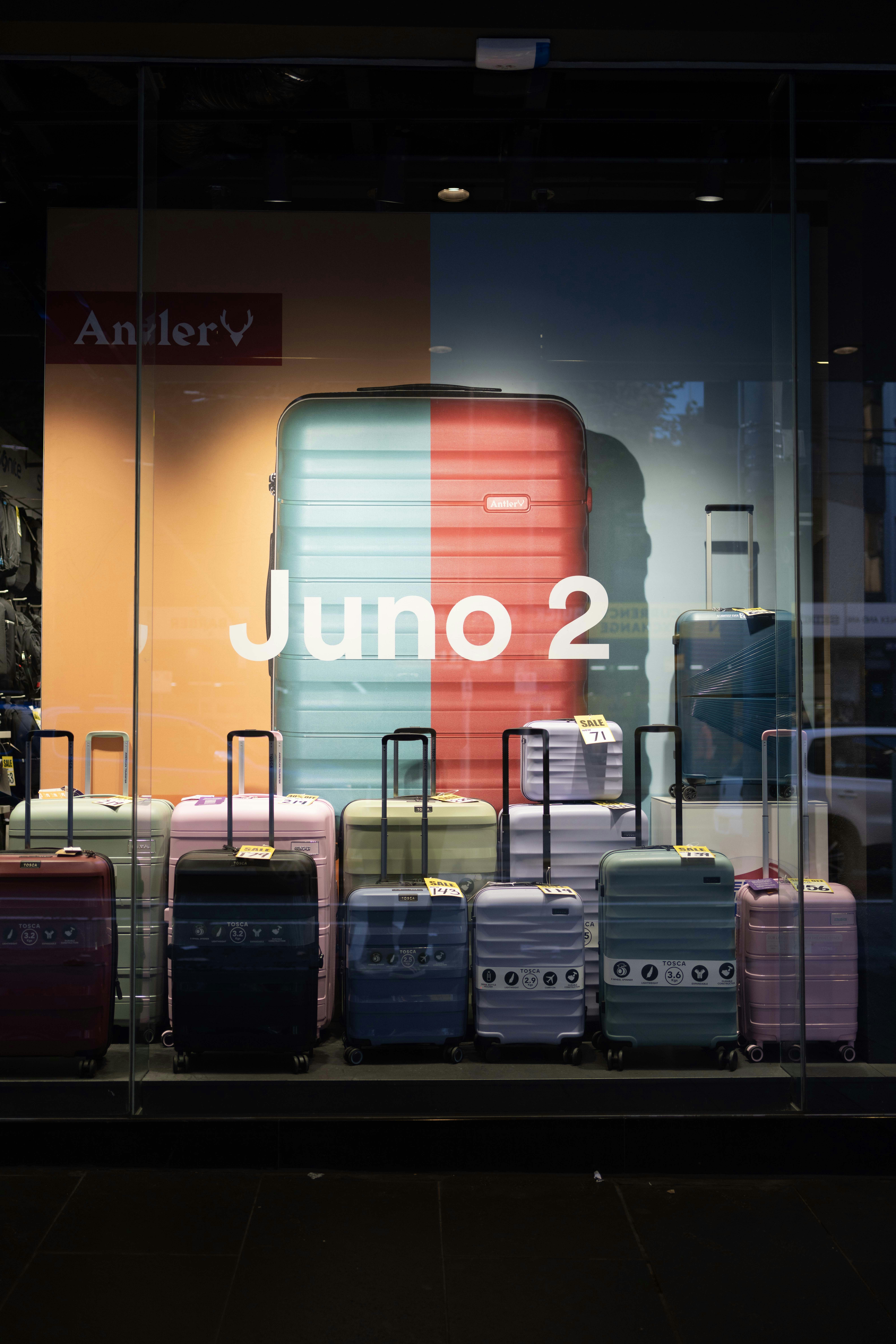 Colorful suitcases arranged in a storefront window, with a bold Juno 2 poster as the backdrop behind glass.