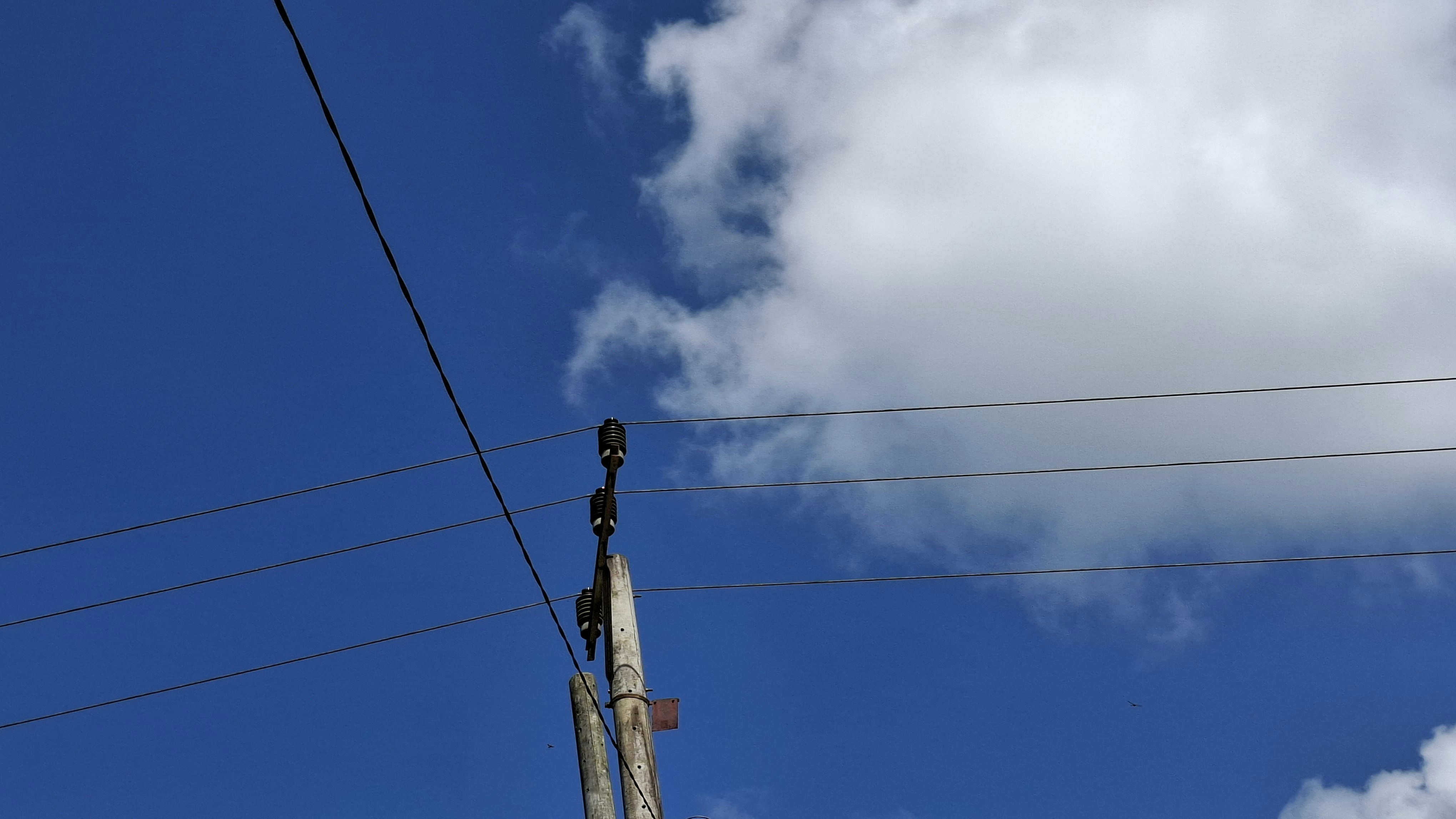 Clear blue sky with a utility pole and wires reaching across the frame, minimal foreground detail and a few clouds.