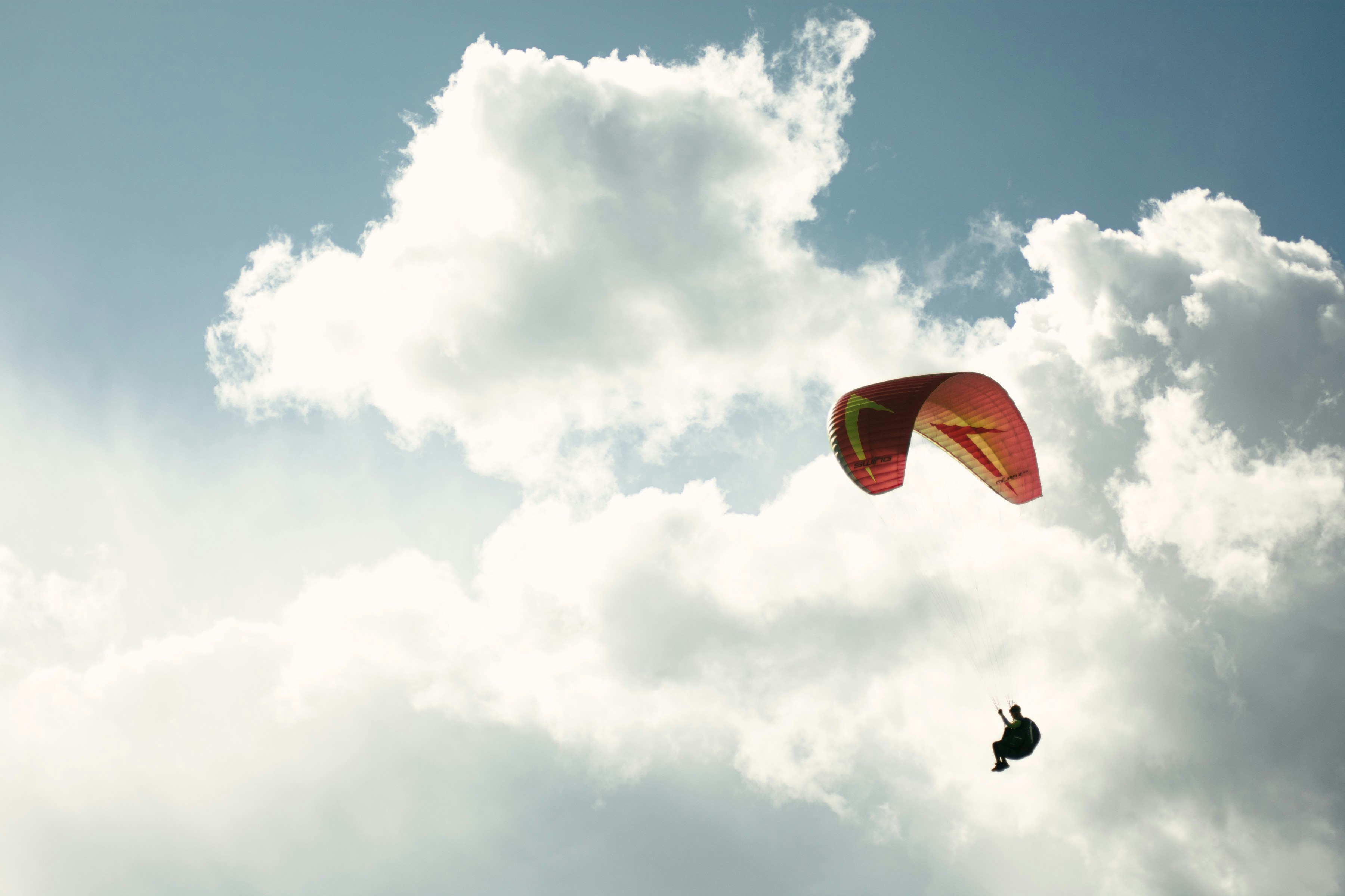 Red Parachute against White Clouds: a lone paraglider suspended in a sunlit sky