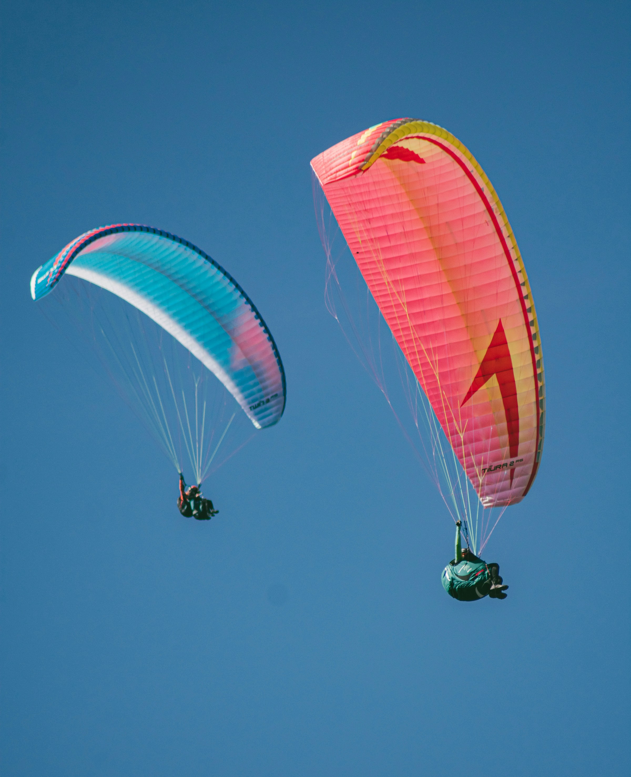 Dual Flyers in a Clear Blue: A Vivid Paragliding Duo Against Sky