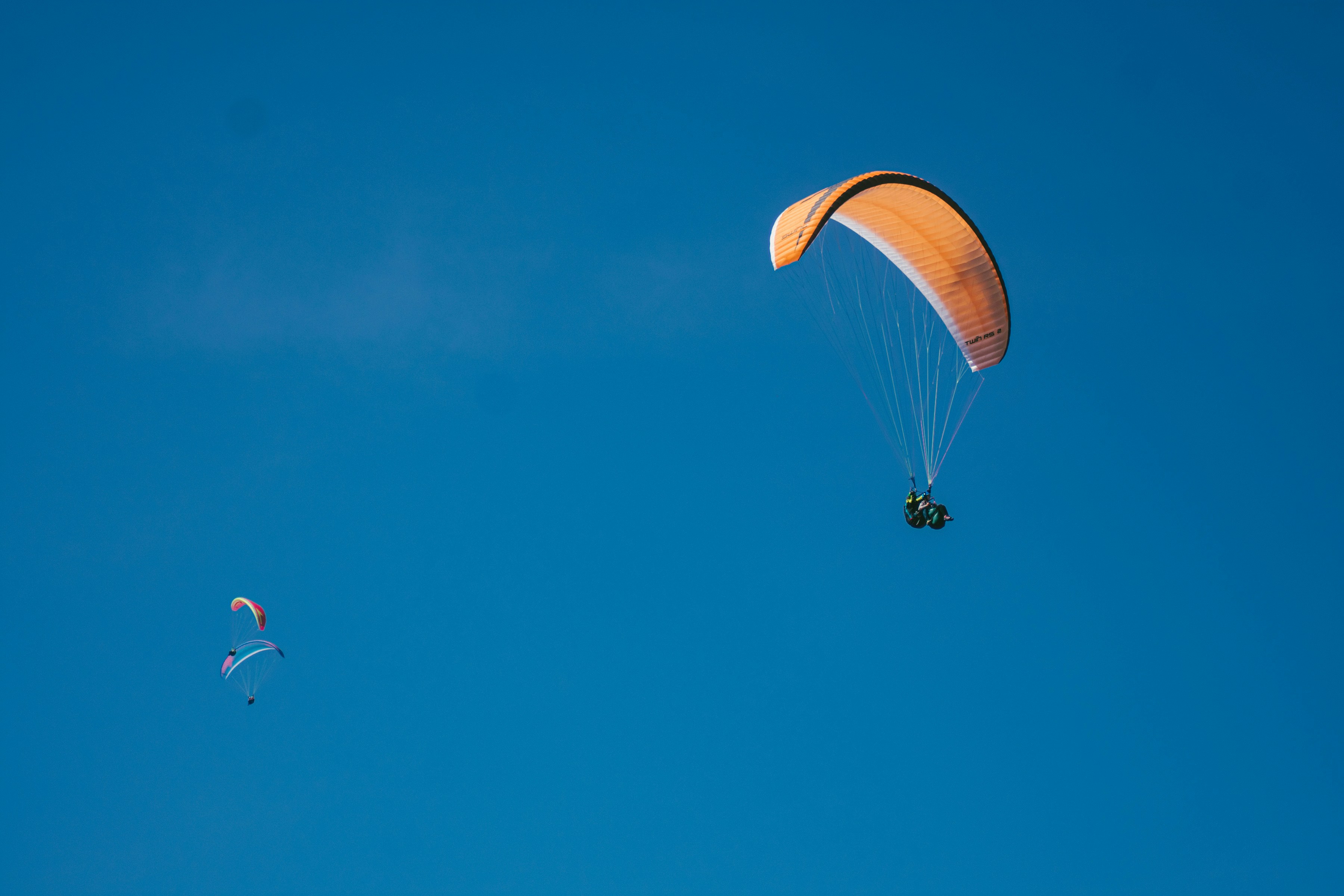 Orange canopy over a tranquil blue sky: a duo of paragliders