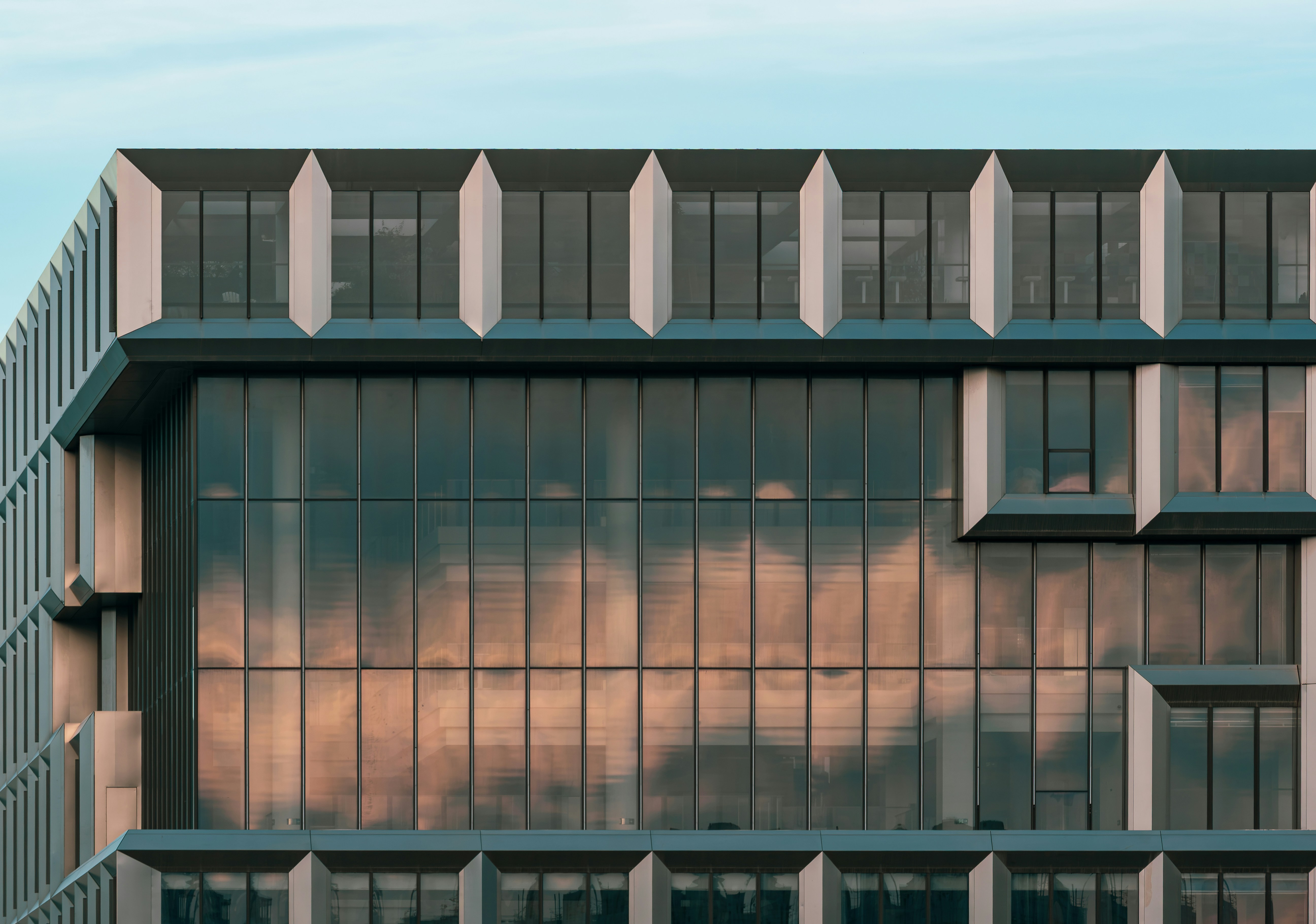 Reflective glass panels mirror a soft sky and clouds, framed by geometric concrete fins across the building’s façade.