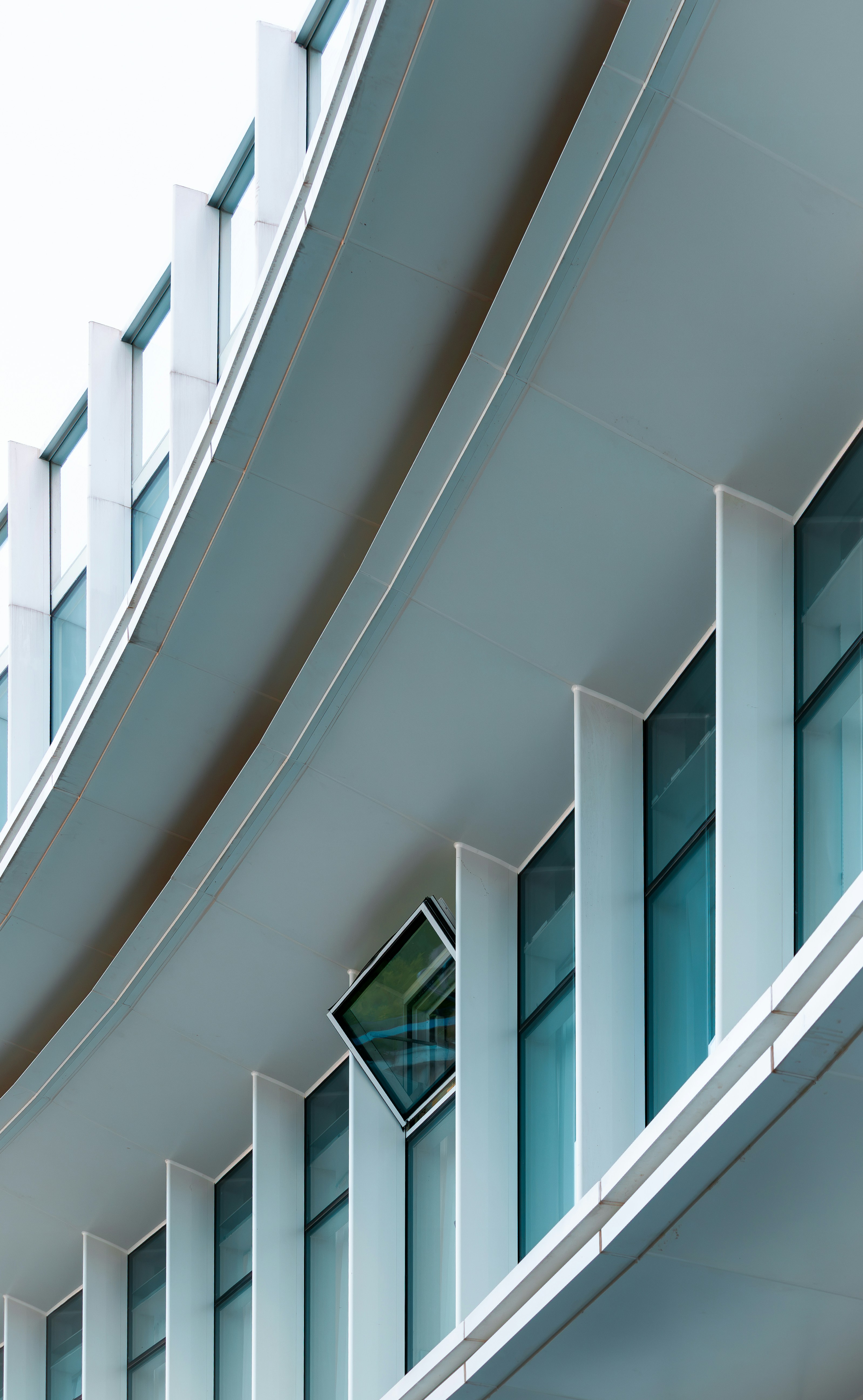 Sleek building facade with diagonal lines, glass windows, and a lone tilted square window feature; architectural detail emphasizing geometry and light.