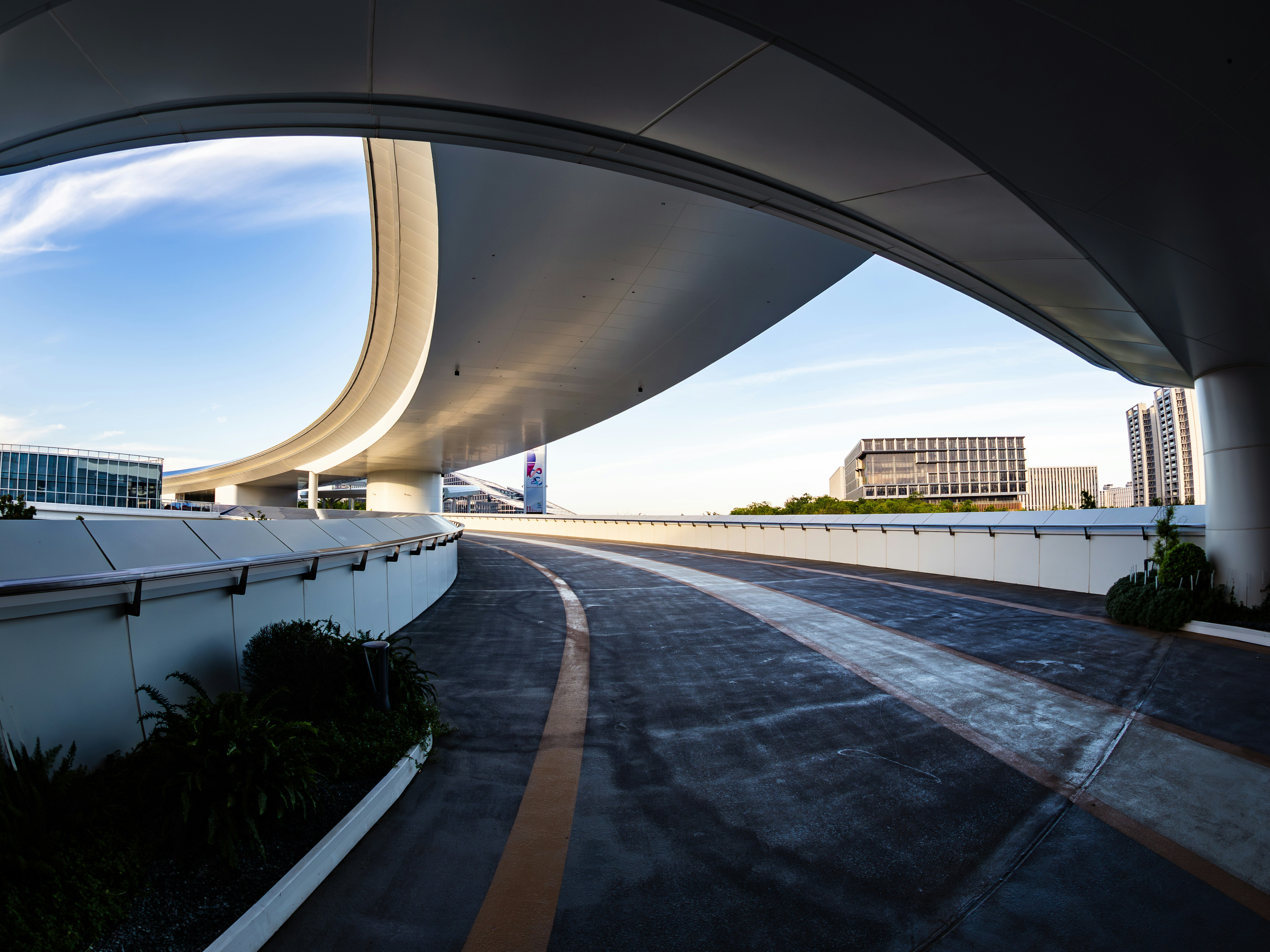  angular concrete overpass curves above a pedestrian path, with a distant cityscape and blue sky; the scene emphasizes structure, motion lines, and the sheltered foreground.