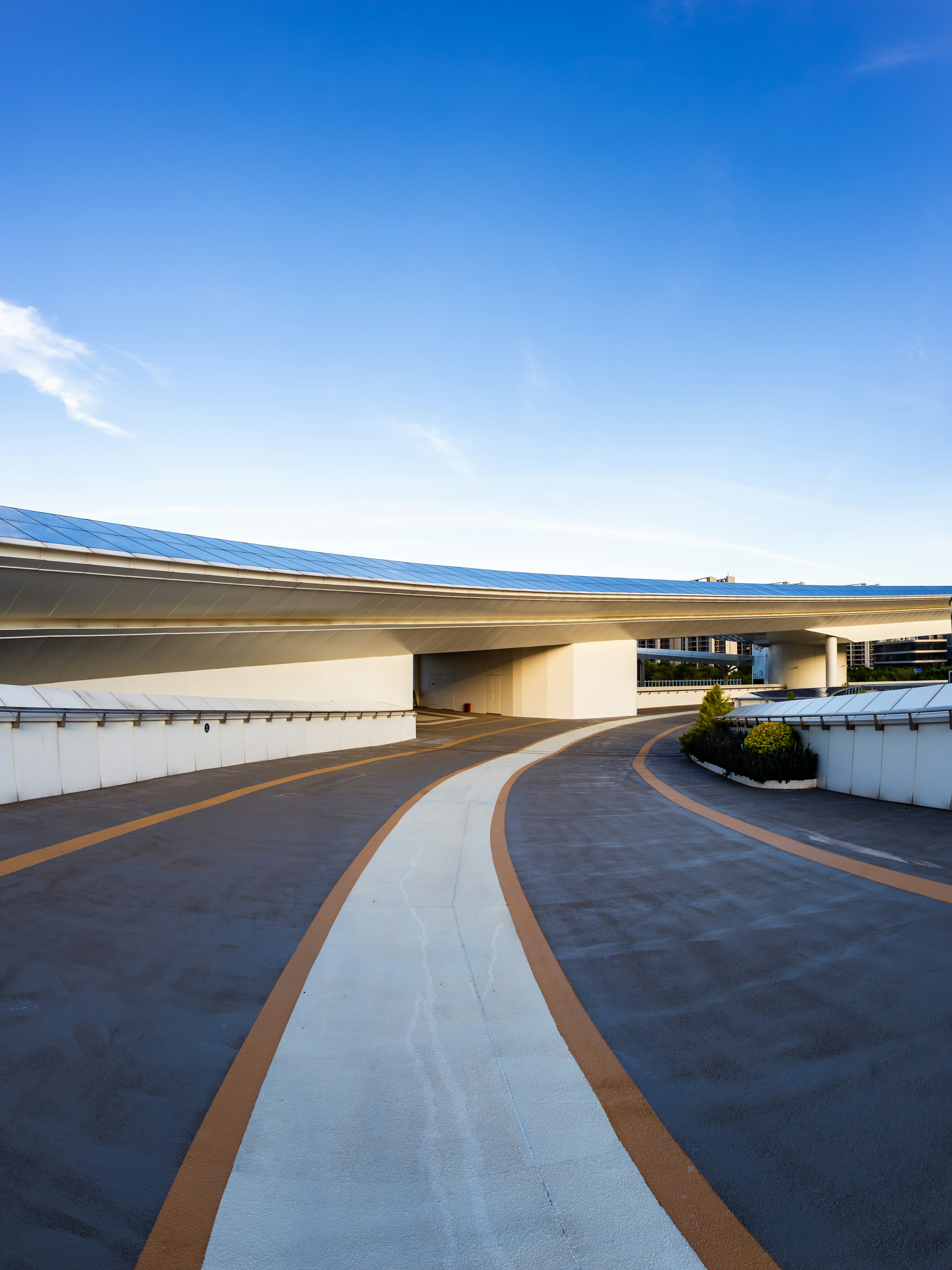 Wide concrete ramp curves beneath an elevated highway against a clear blue sky; lanes and a railing lead the eye toward a distant horizon.